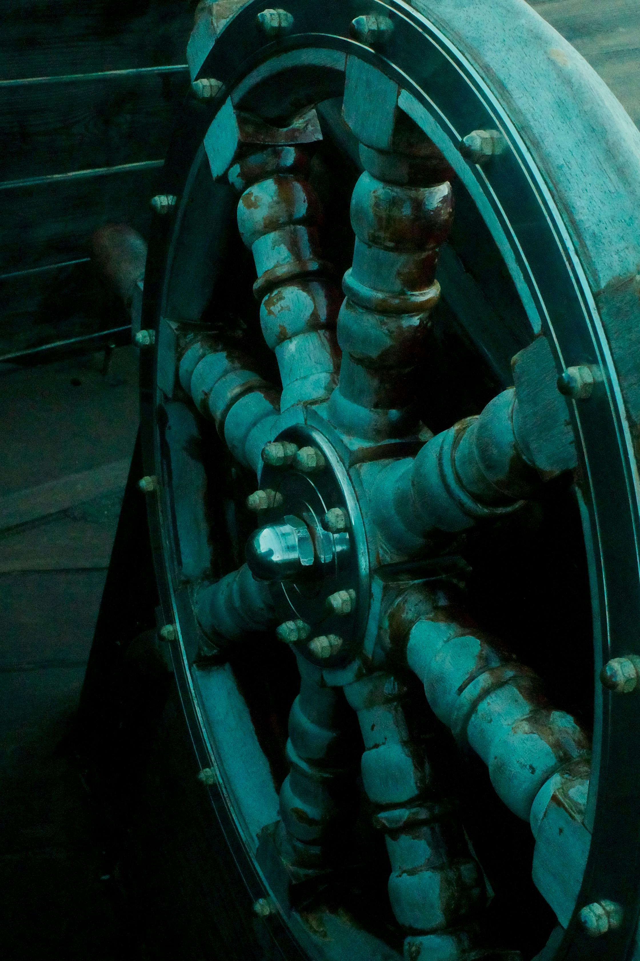Rusted machinery wheel: turquoise facets and bolted spokes in moody blue light