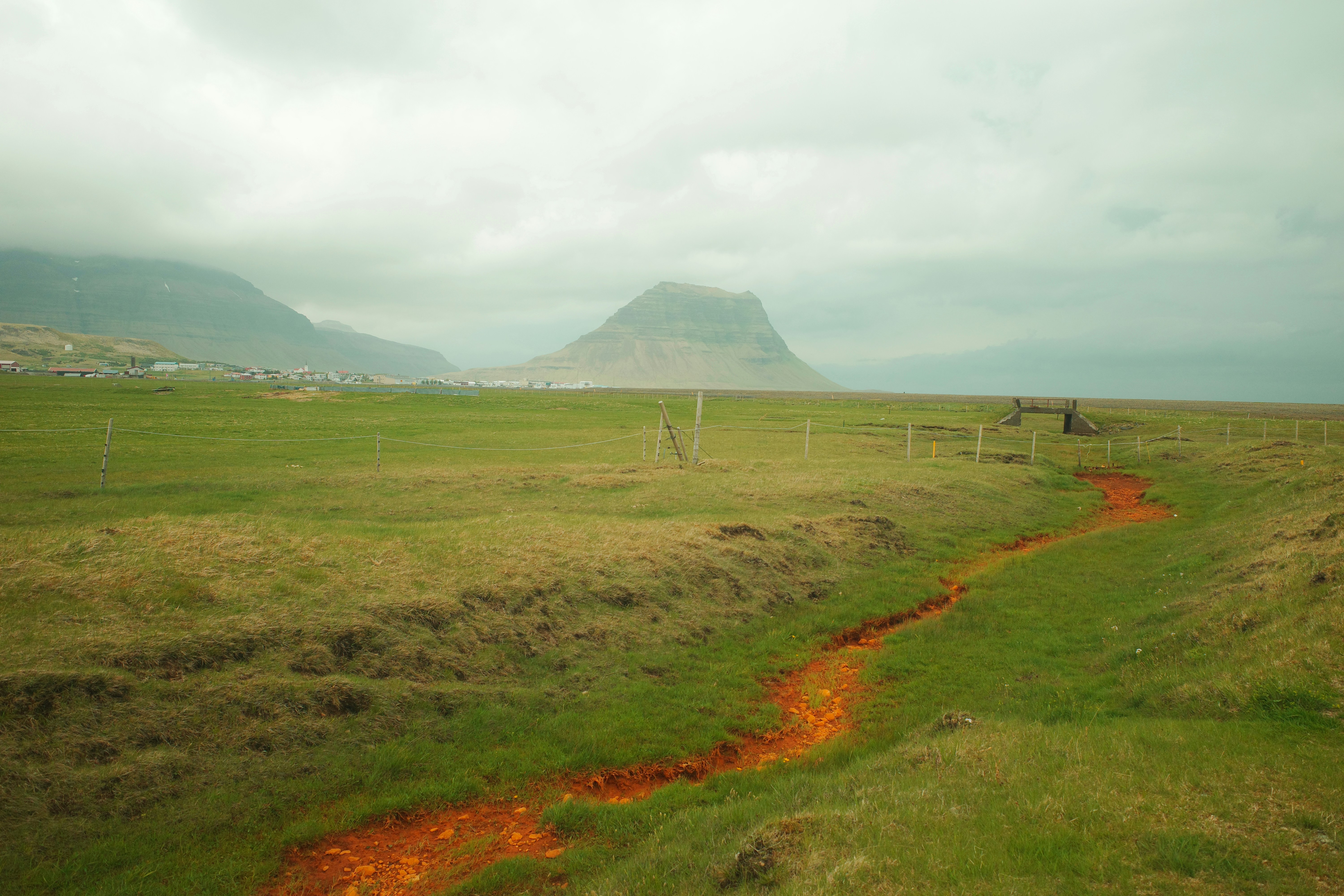 Rusted Creek Meanders Through Open Grasslands Toward Distant Mountains
