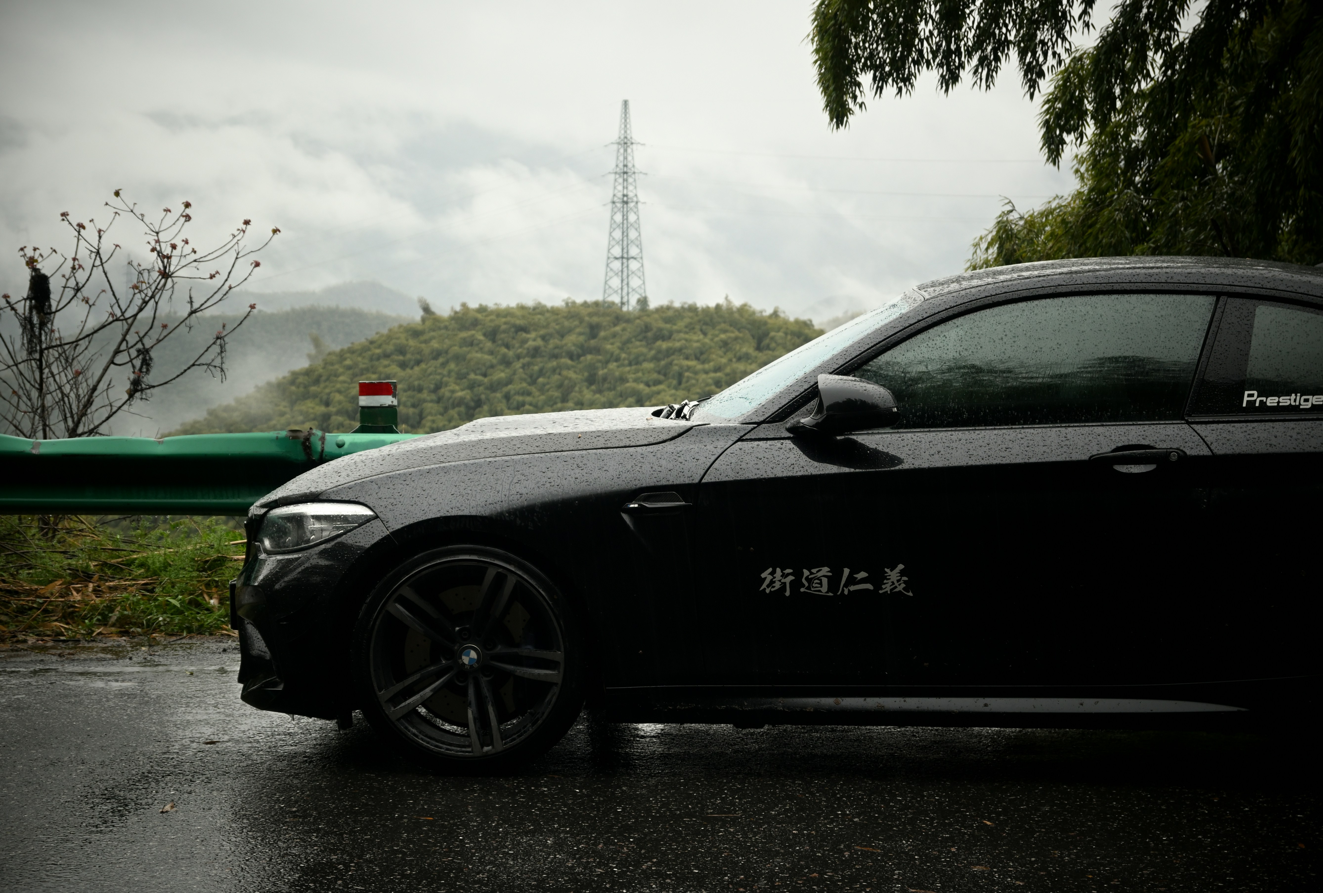 Dark sedan by a rain-soaked roadway with distant hills