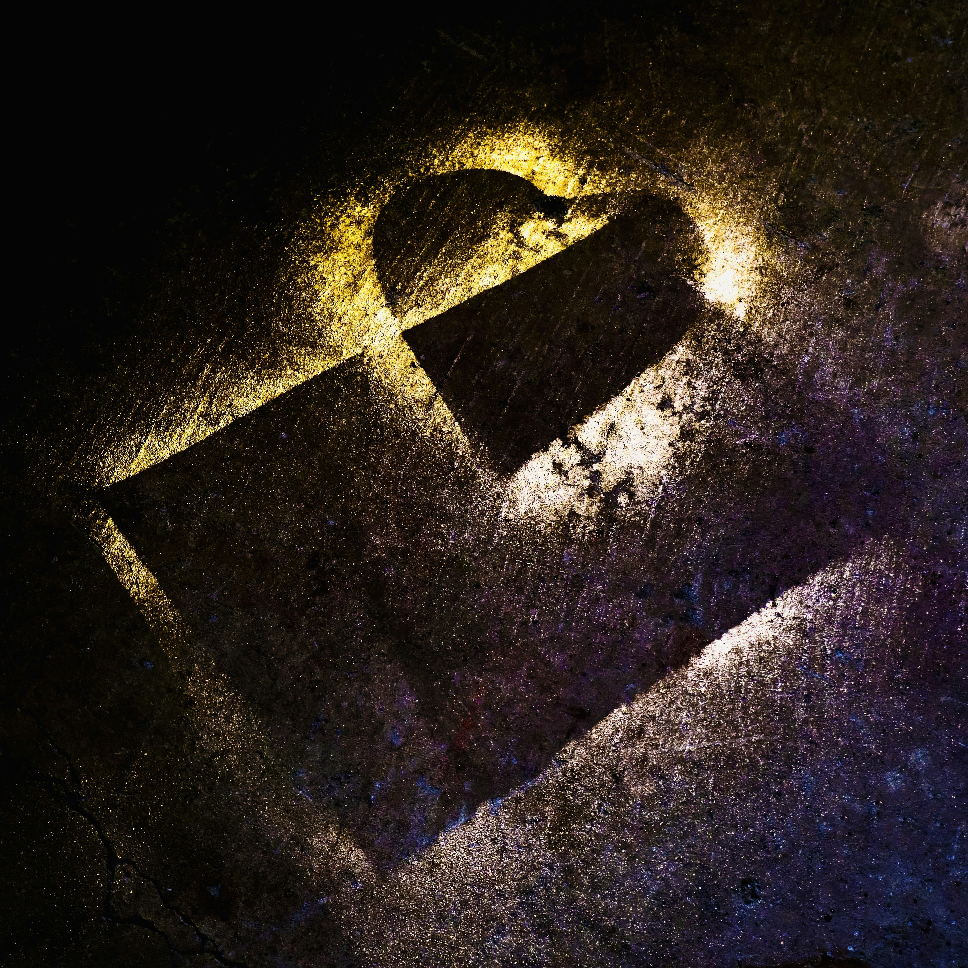Abstract dark composition featuring a softly illuminated geometric heart shape within a textured, gritty surface; an artistic, almost industrial light canvas.