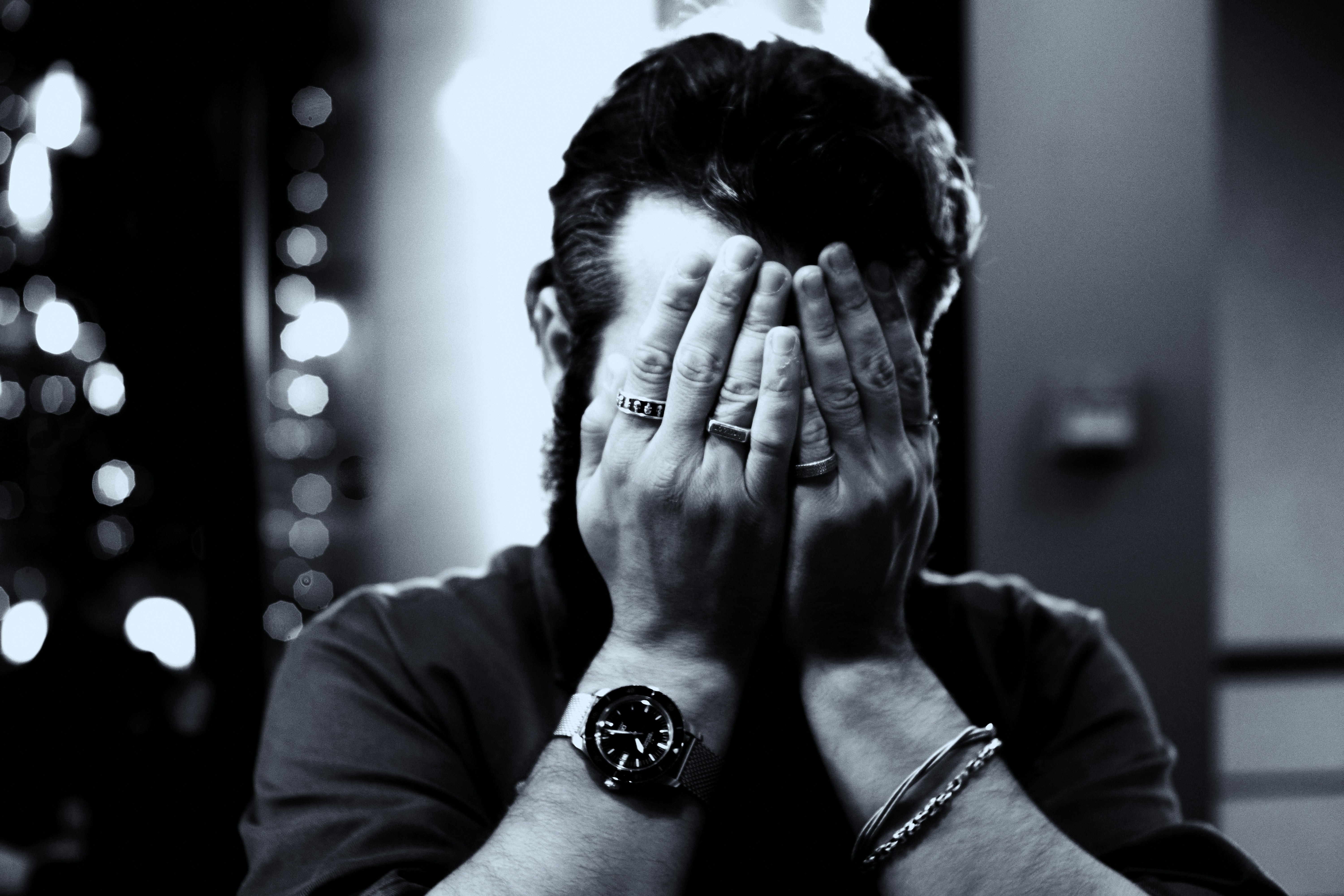 A person covers their face with hands, wearing a watch.