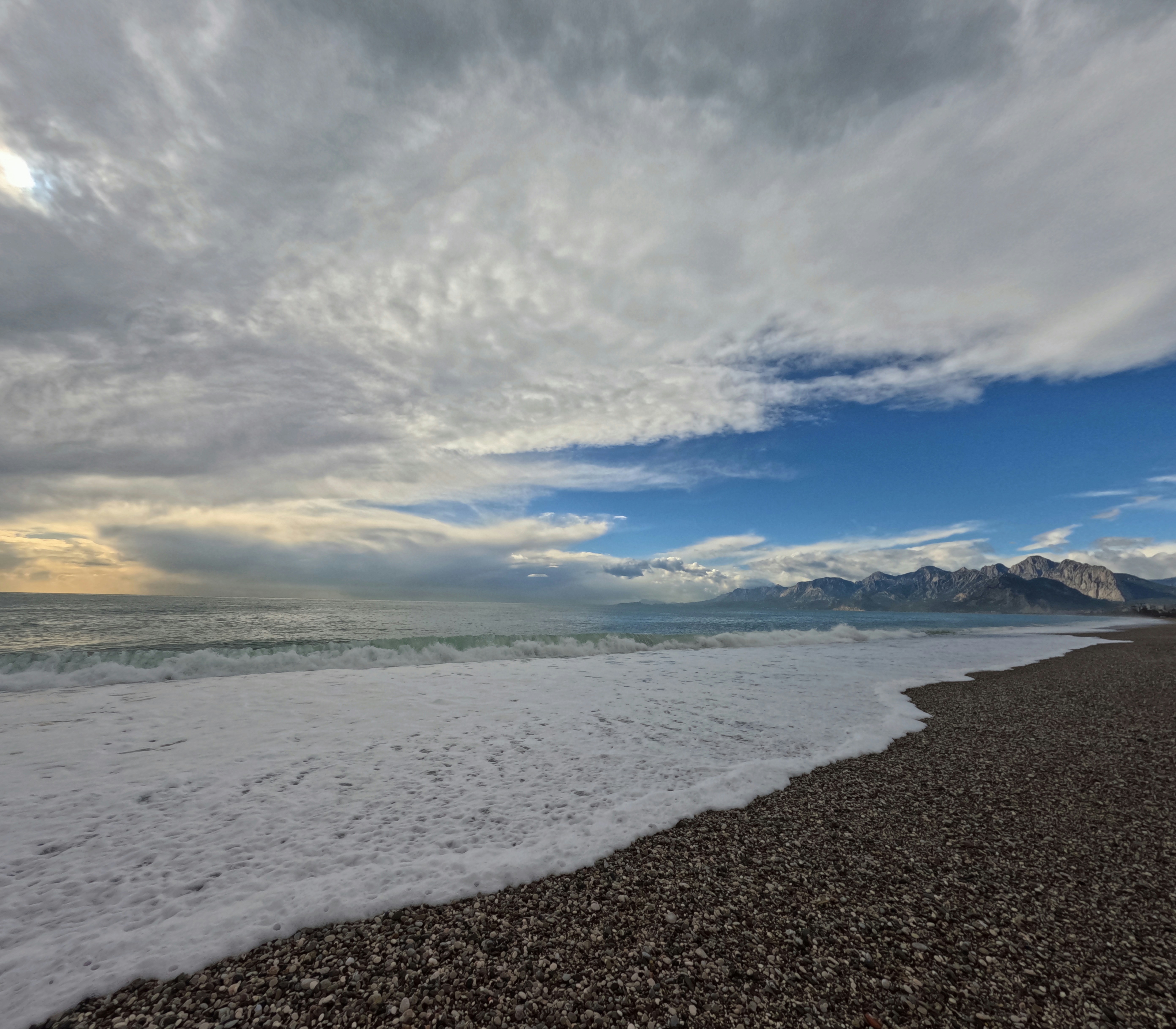 Foamy shoreline meeting distant alpine horizon under a dramatic sky