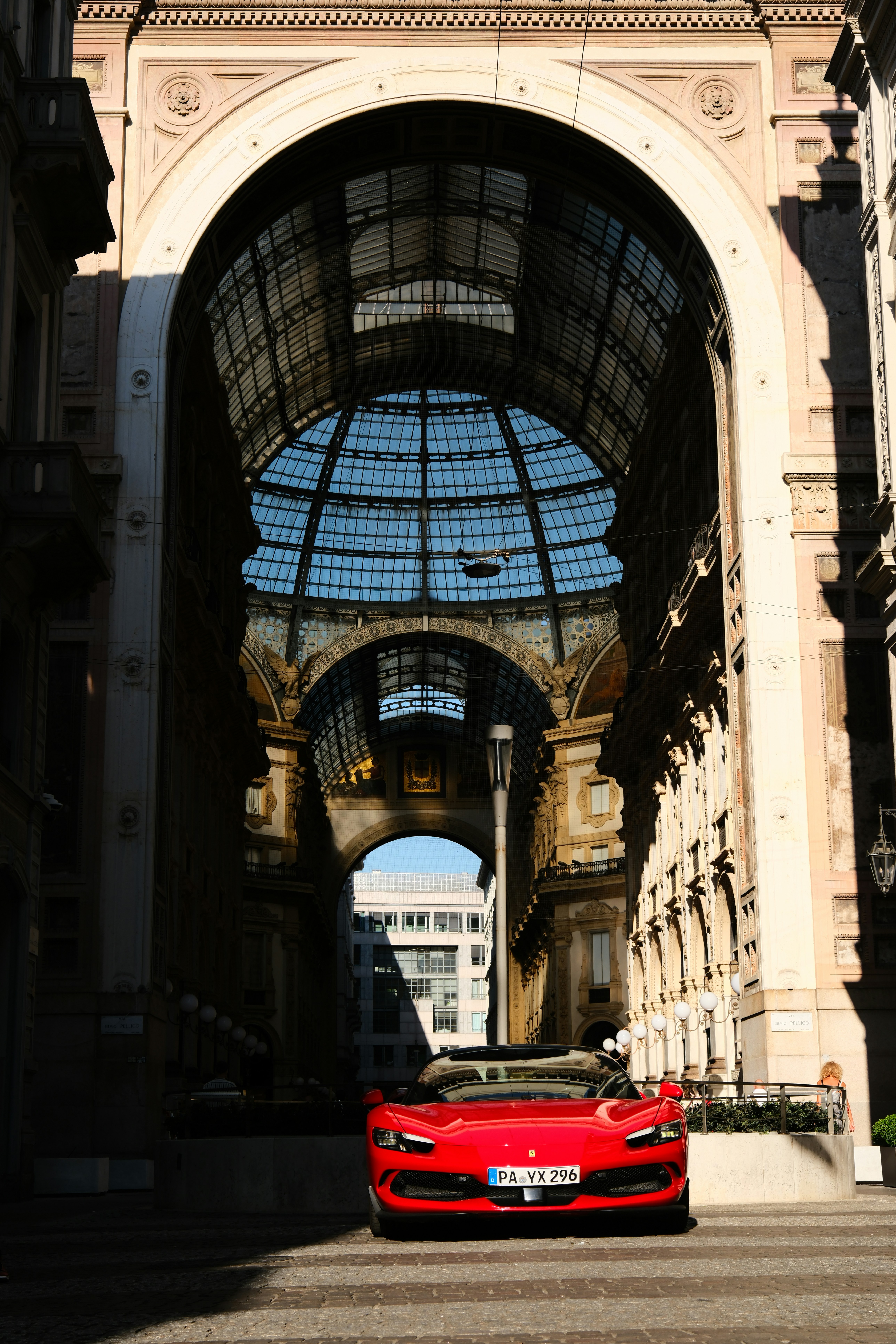 A vivid red sports car sits beneath a grand glass archway, framed by ornate stonework and deep shadows, highlighting contrast between modern automotive design and historic architecture.