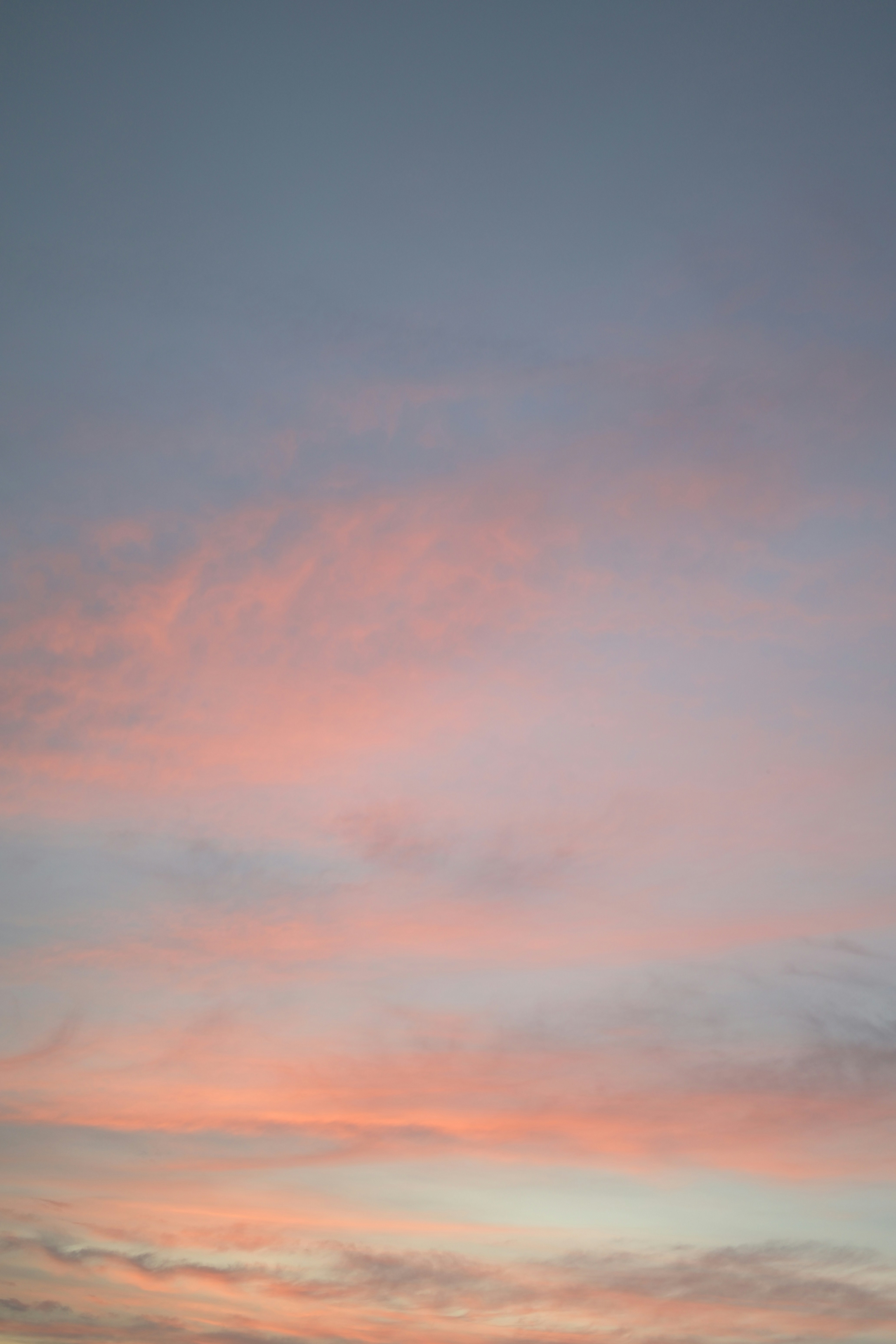 Soft pastel clouds drift across a serene sunset sky, with warm pinks blending into cool blues. A tranquil, cloud-filled horizon offers a calm, cinematic moment.