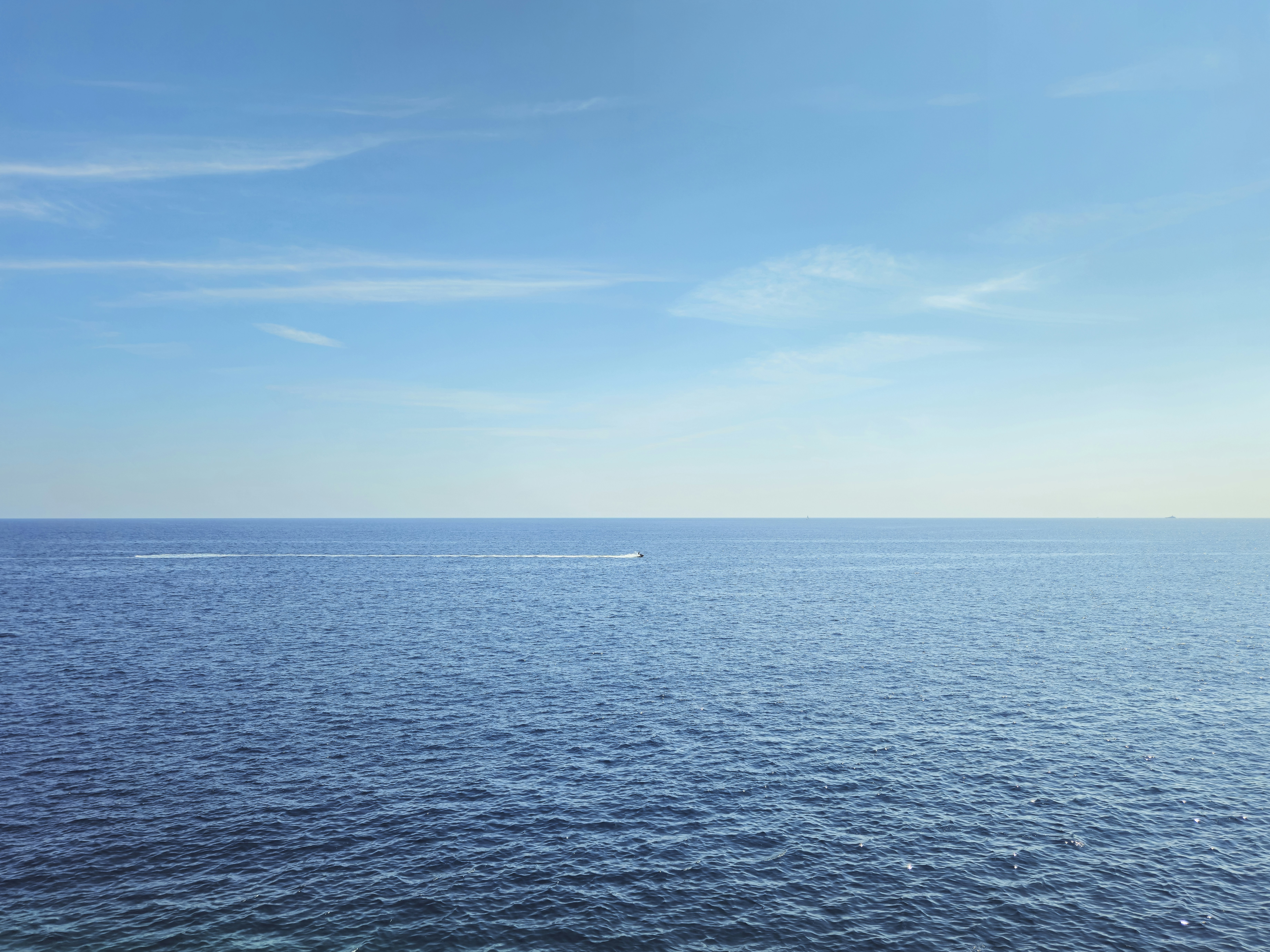 Calm ocean stretches to a distant horizon under a bright blue sky; minimal foreground detail emphasizes expanse and serenity. (landscape photograph)