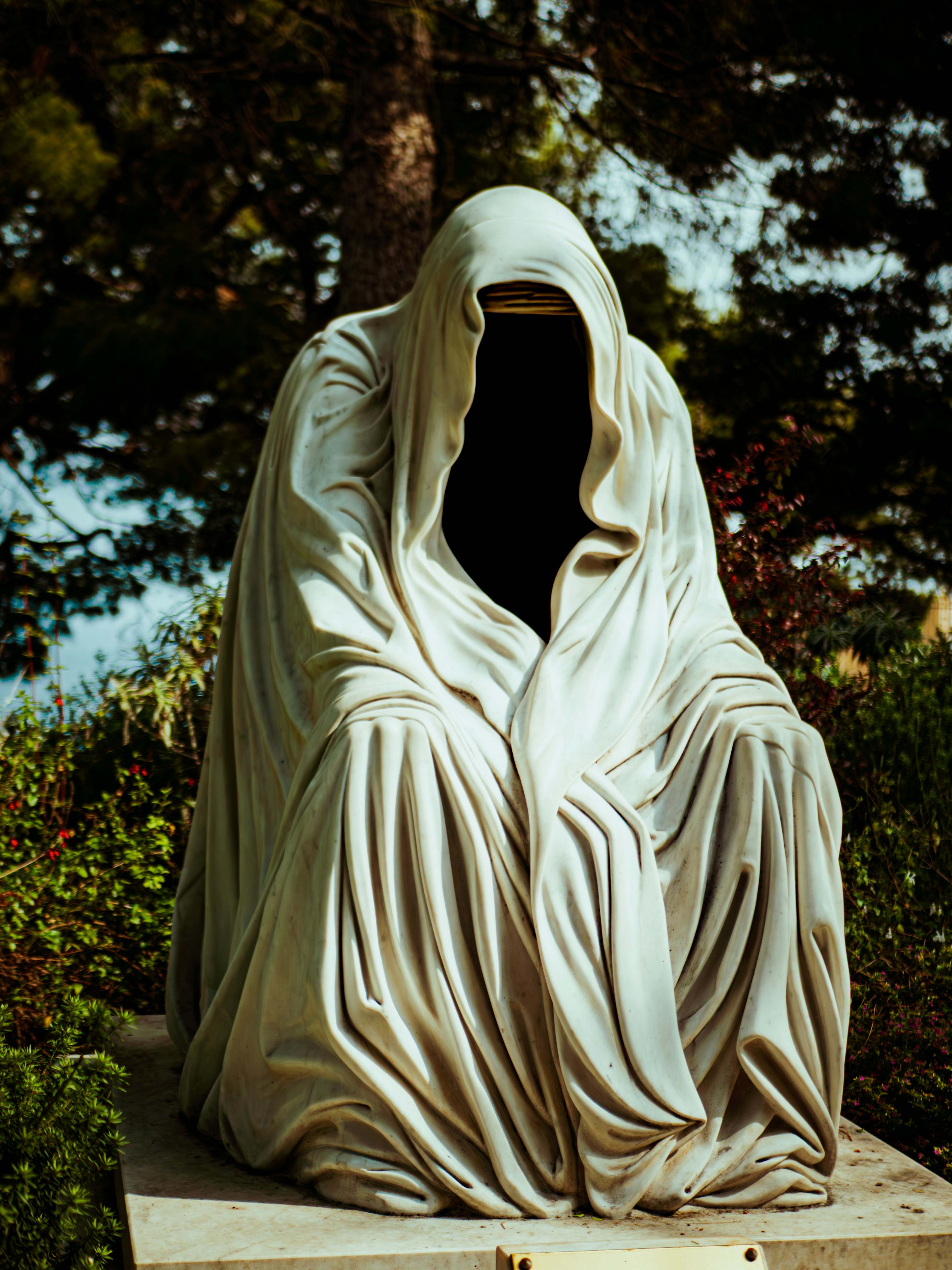 The Veiled Sentinel: A Hooded Statue Amid Garden Light