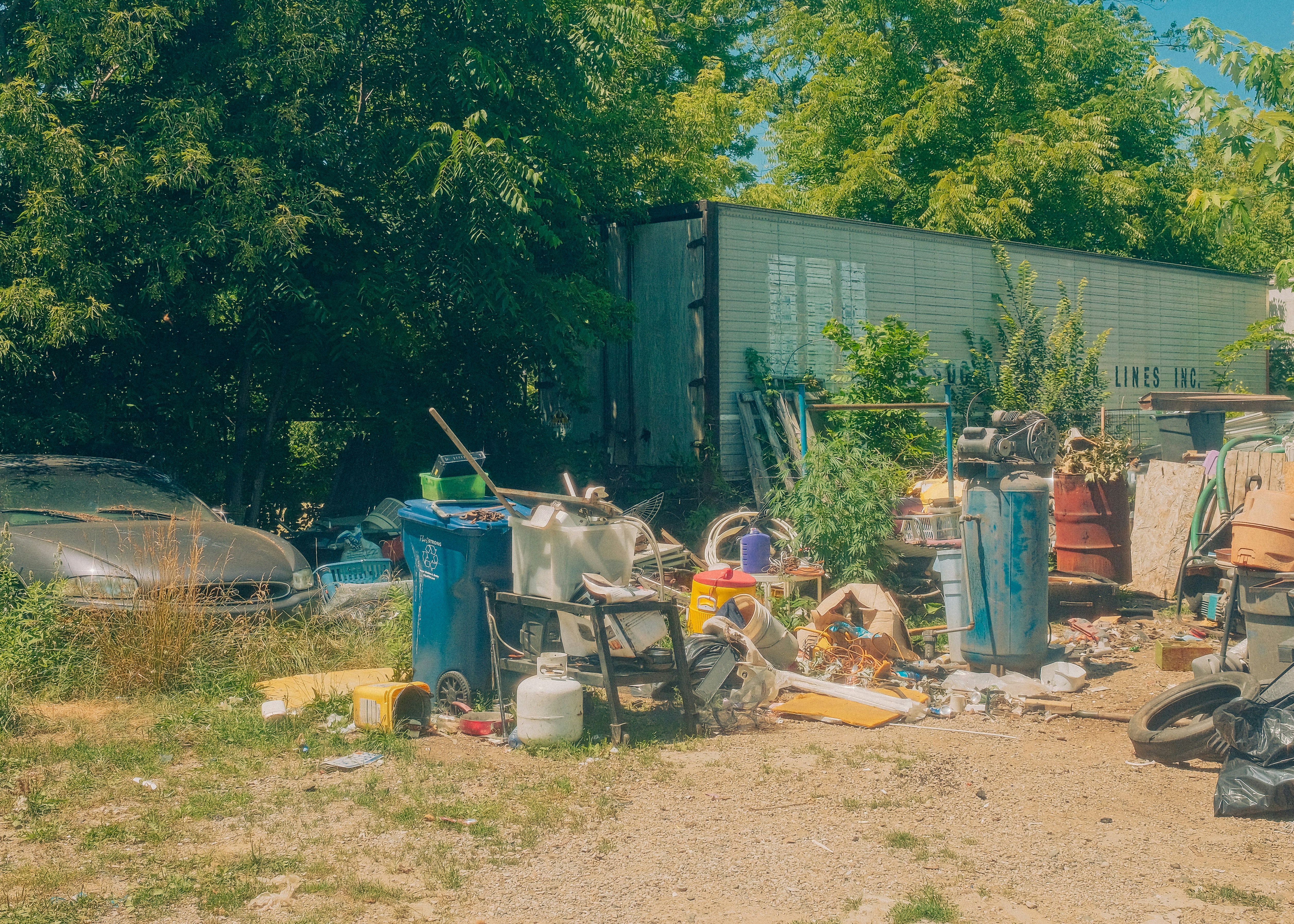 Pile of discarded debris by a weathered trailer at the edge of a sunlit yard