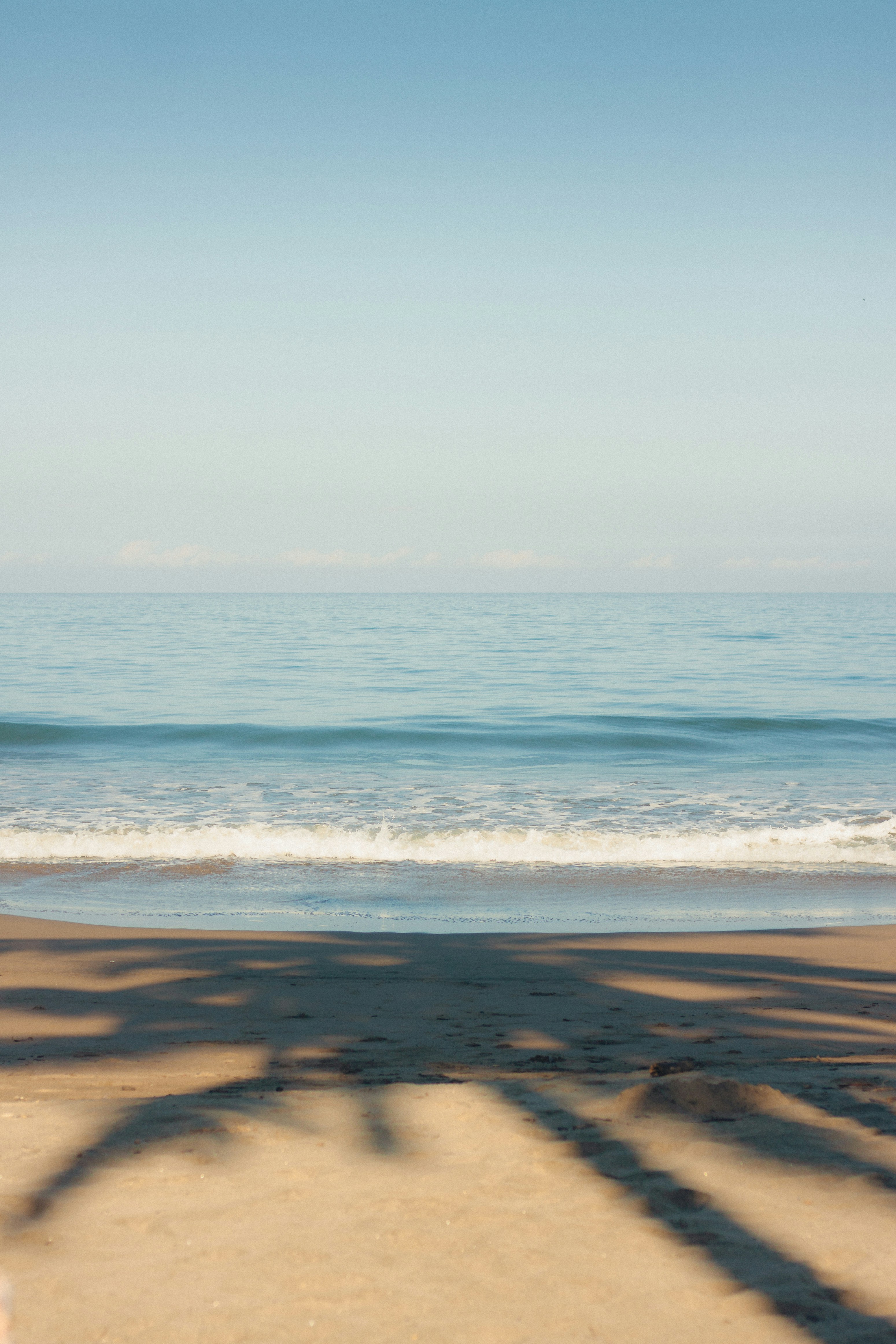Sunlit Shoreline: Quiet Ocean Under a Pale Sky