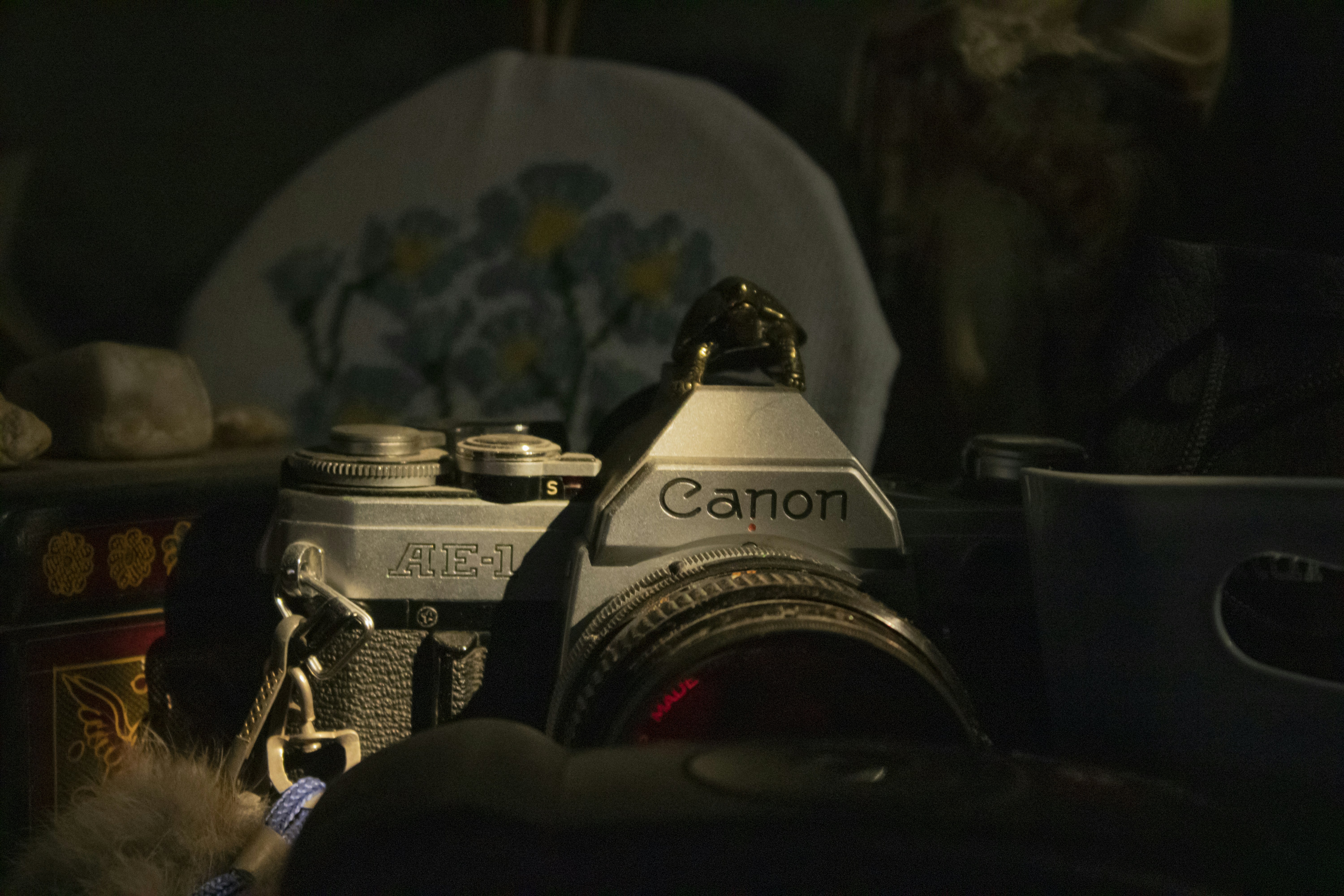 A vintage Canon film camera sits on a cluttered surface with other gear and a soft, dark background, highlighting its retro design.