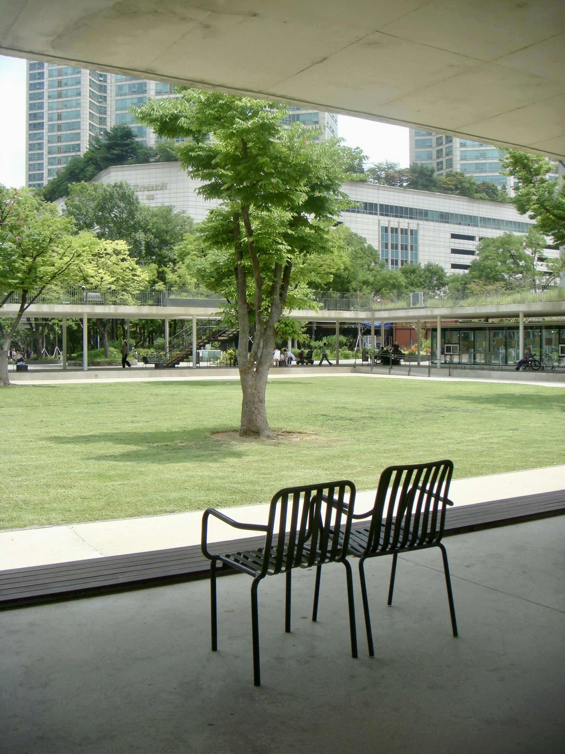 Two black chairs overlook a green courtyard and modern buildings.