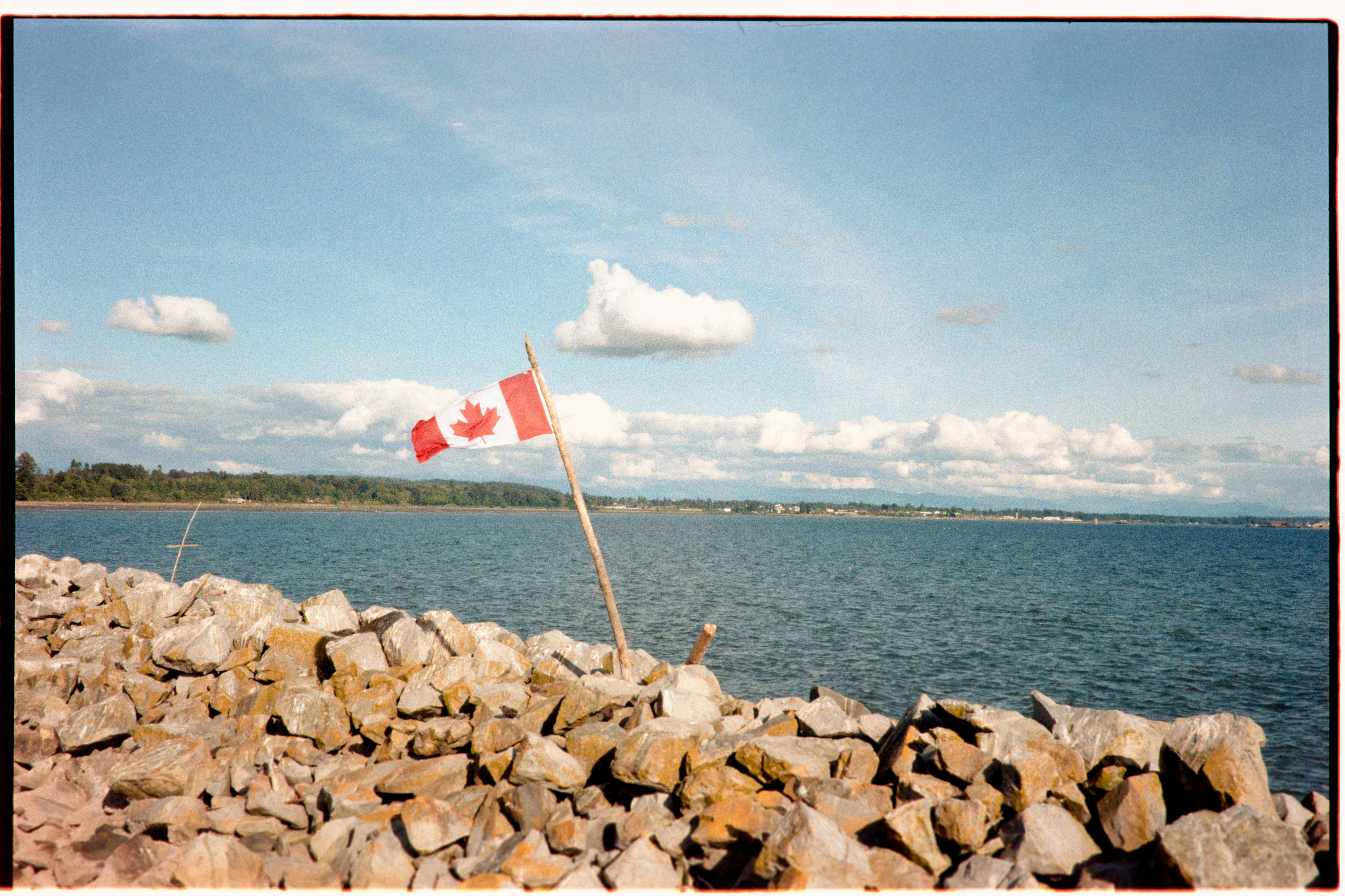 Canadian Flag on a Rocky Breakwater Overlooking a Calm Lake