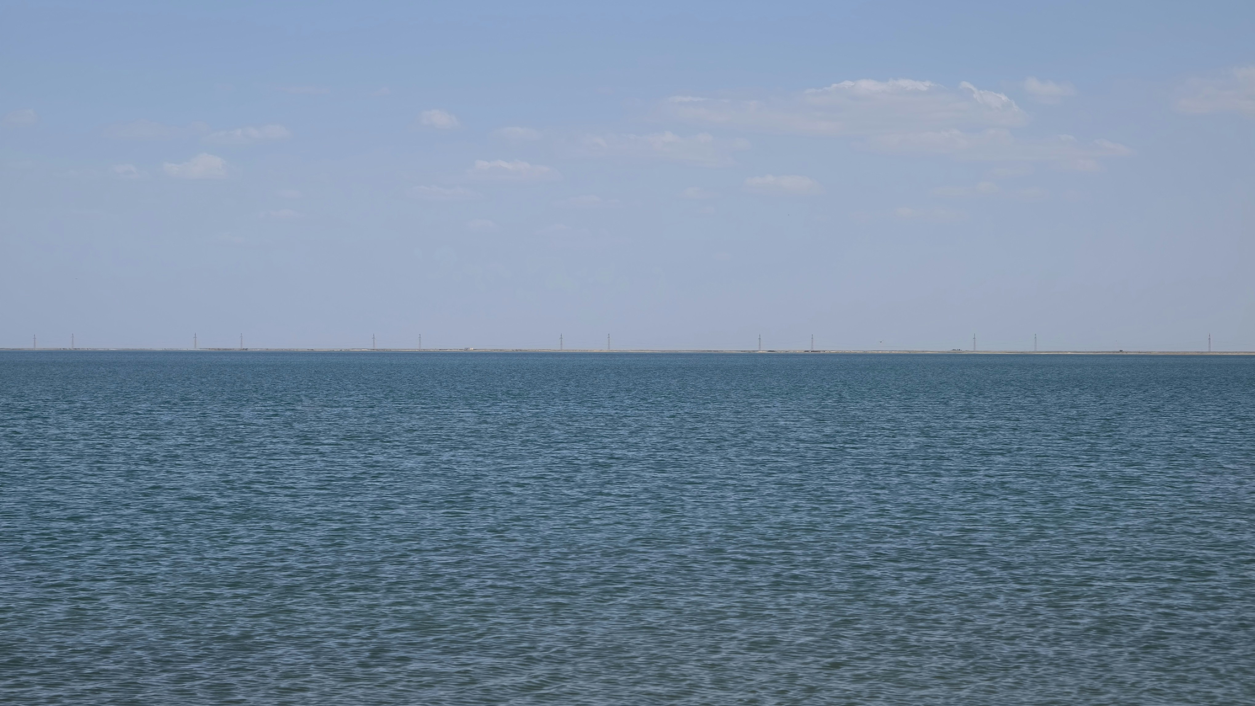 A tranquil seascape with a distant horizon over blue-green water and a clear sky, emphasizing vast horizontal calm. This is a straightforward landscape capture.