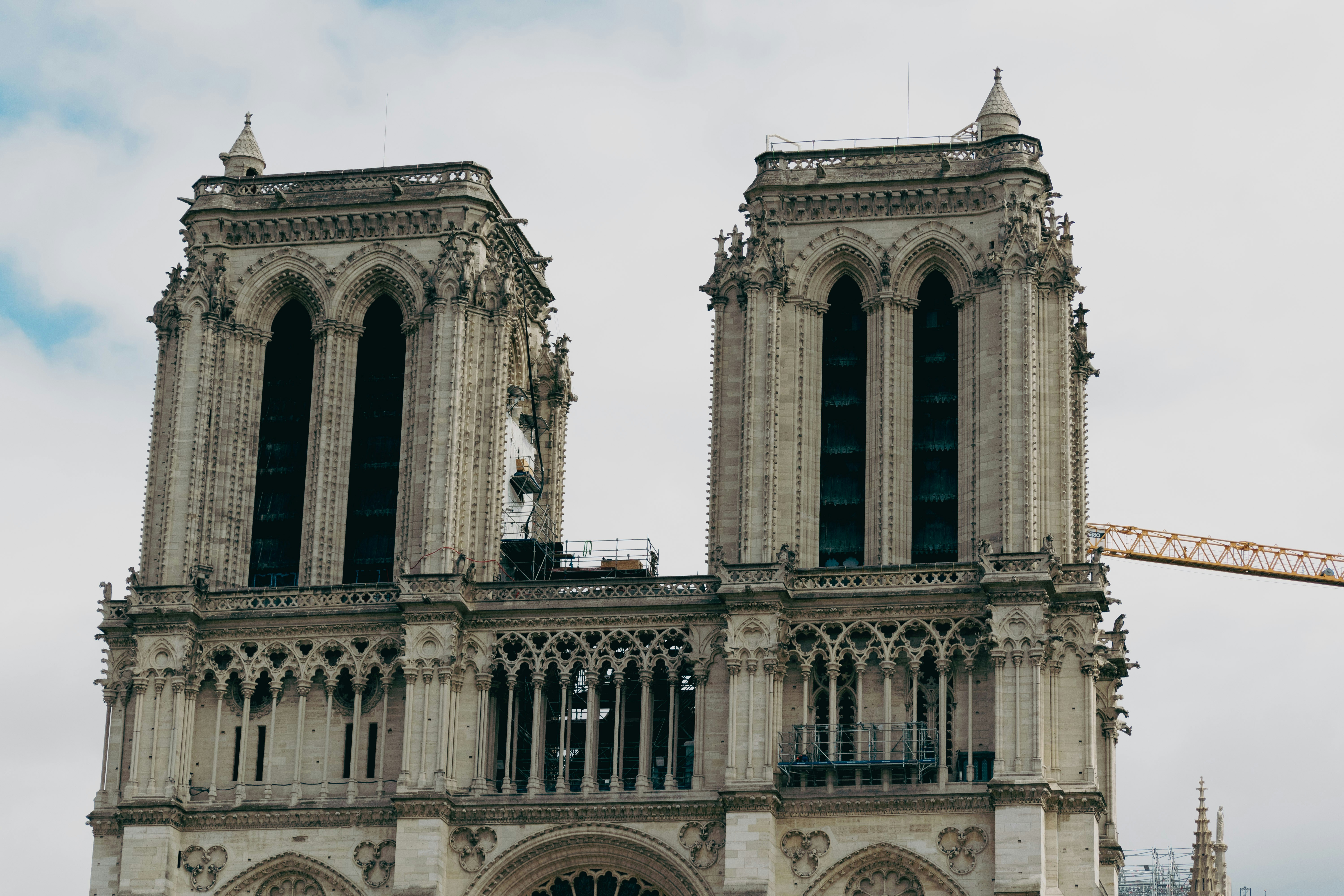 Notre-Dame cathedral’s façade with its twin towers, showing ongoing restoration near the right tower and a crane in the background.