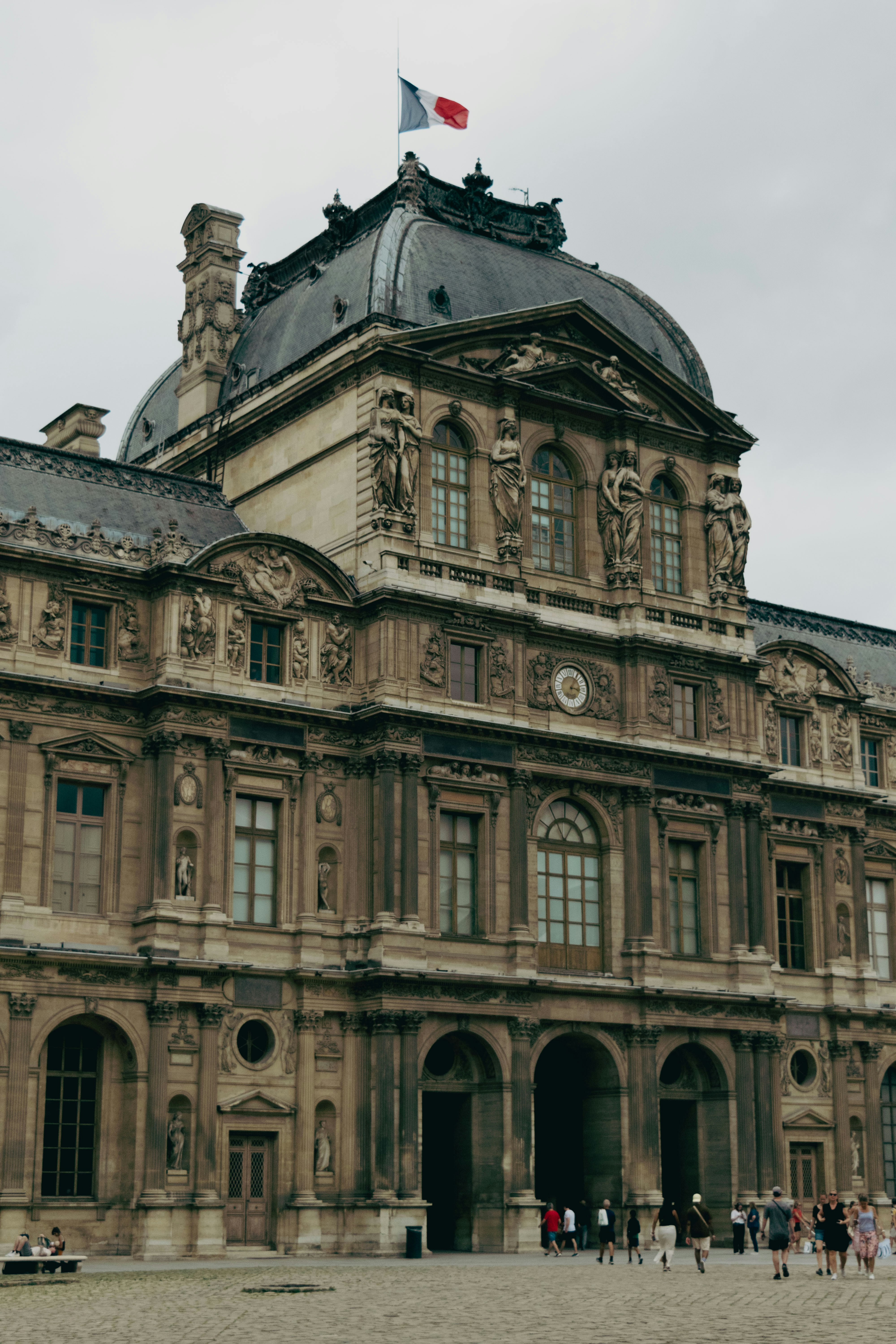 Louvre-like Facade: Stone Carvings and Archways Under a French Flag