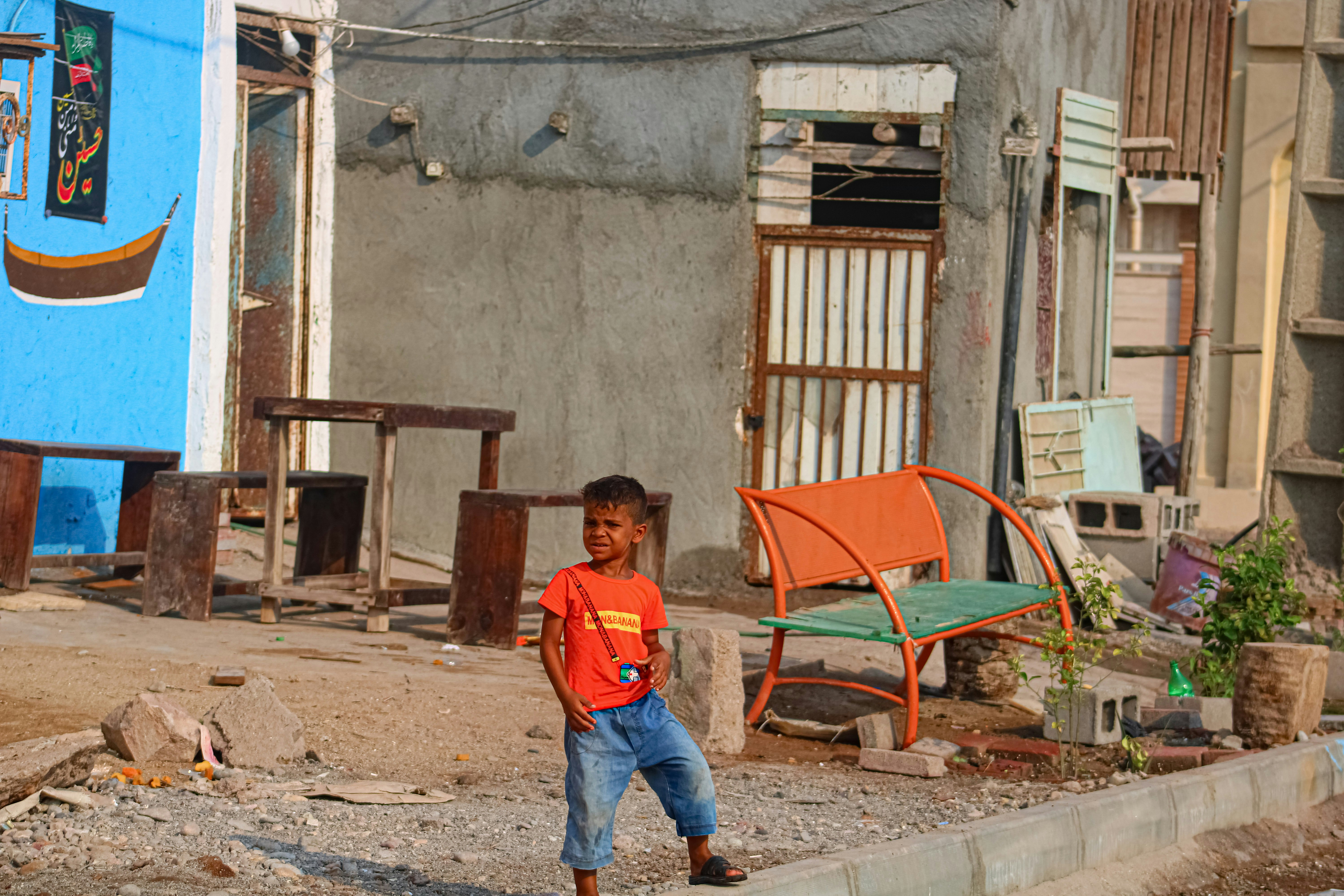 Child in a sunlit alley amid debris and colorful street furniture