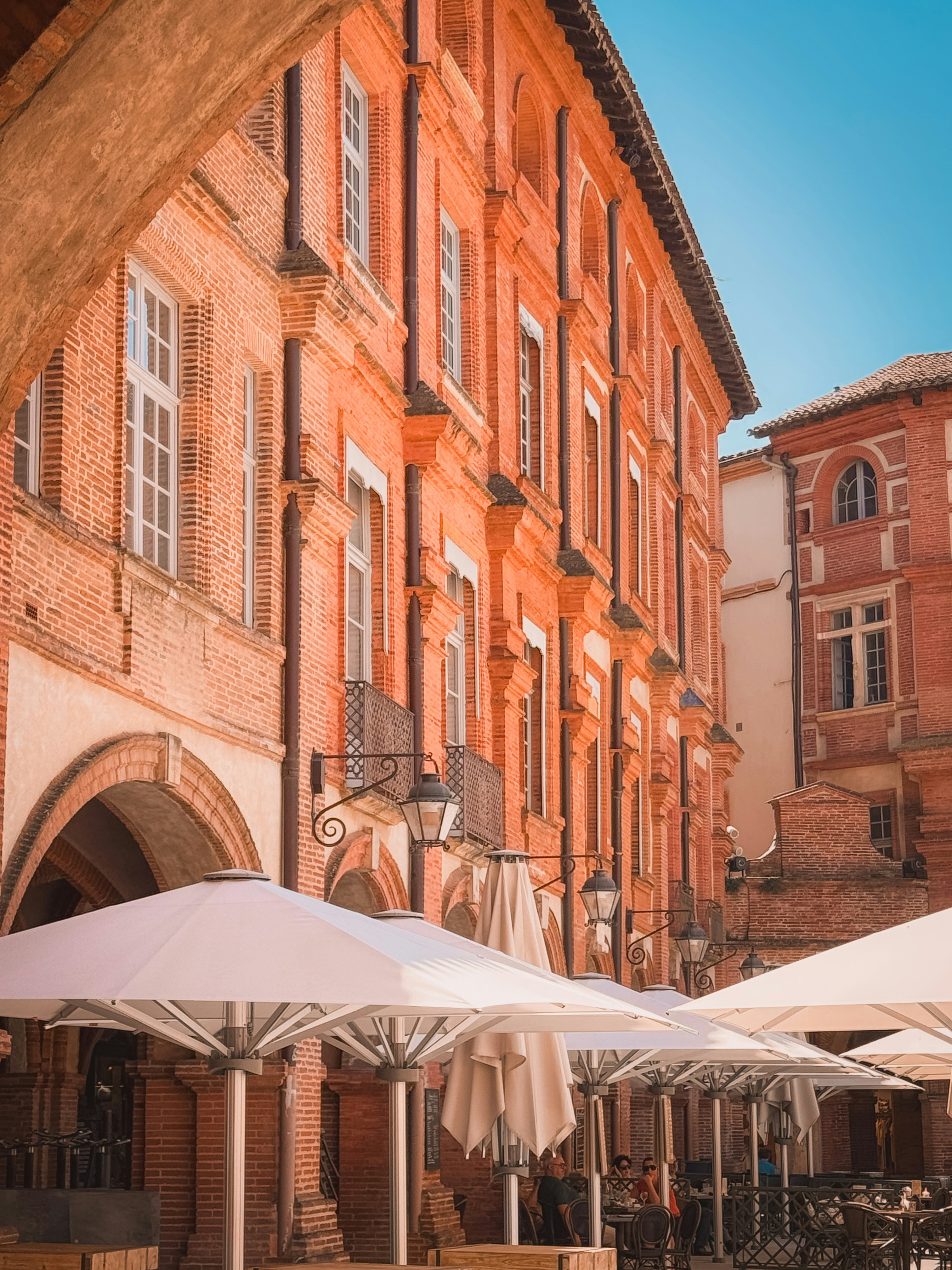 Sunlit Brick Arcade with Café Patio under Pale Blue Sky
