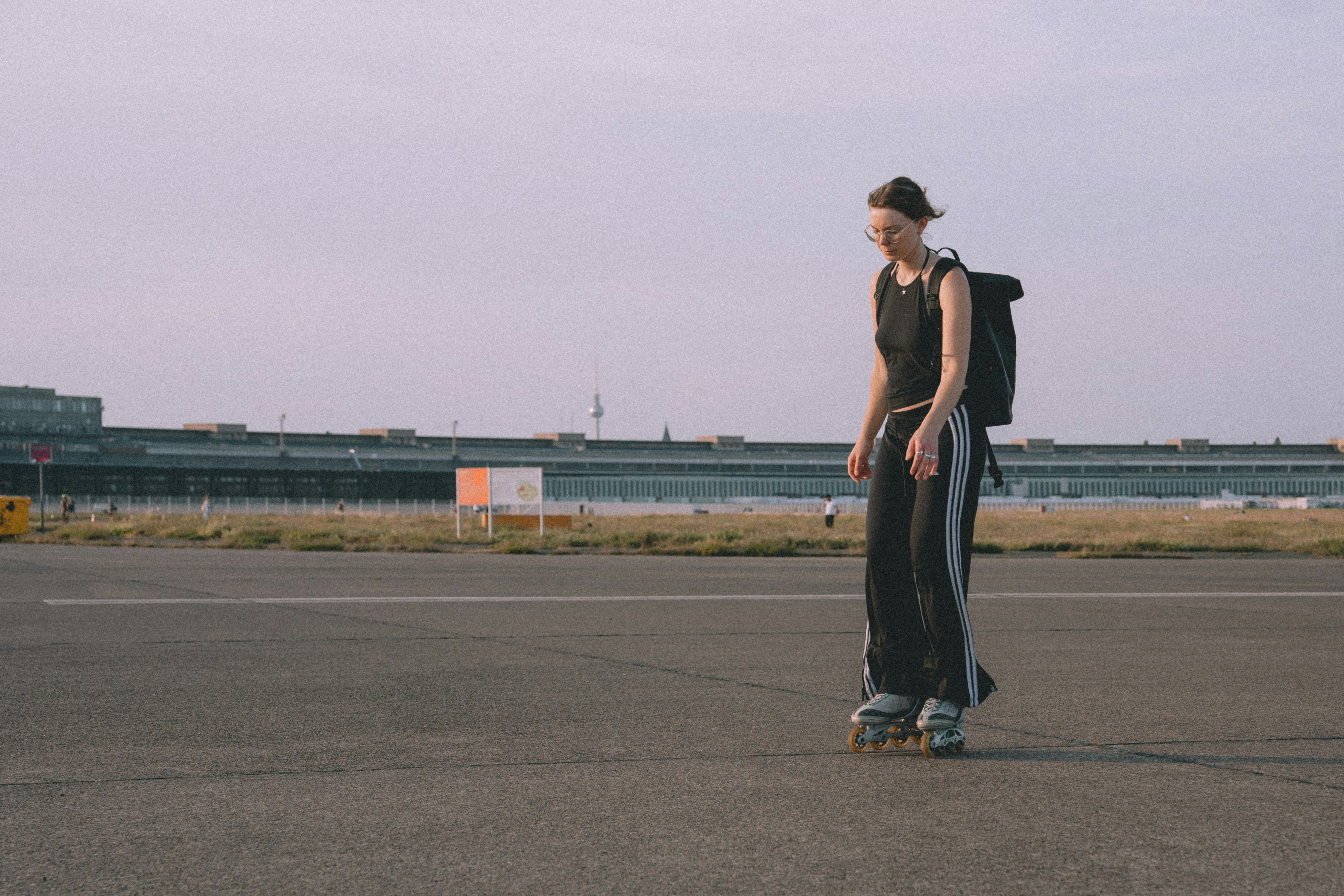 Roller skater on an empty tarmac at dusk with a backpack ready to roll
