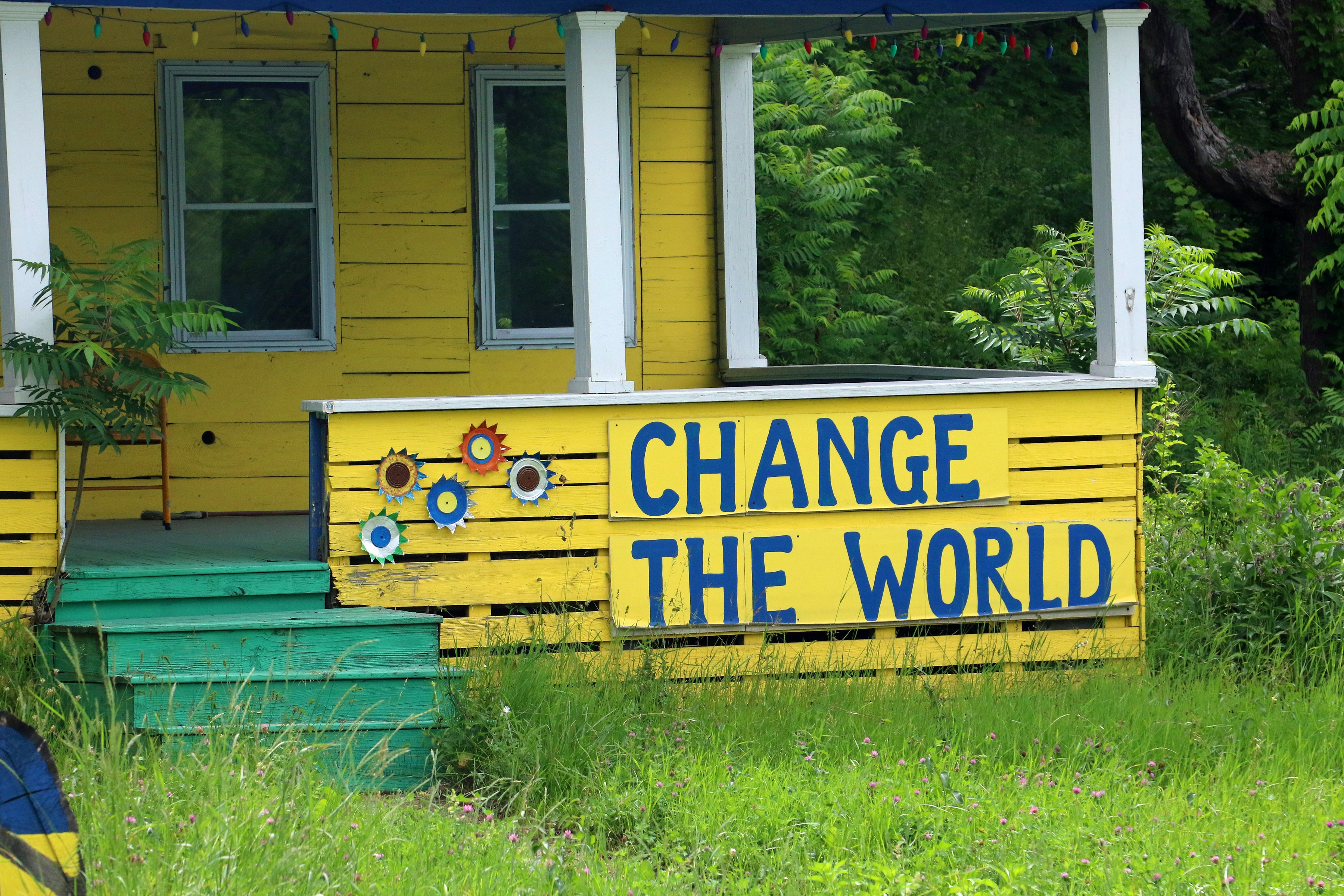 Yellow cabin with Change the World sign under a leafy canopy