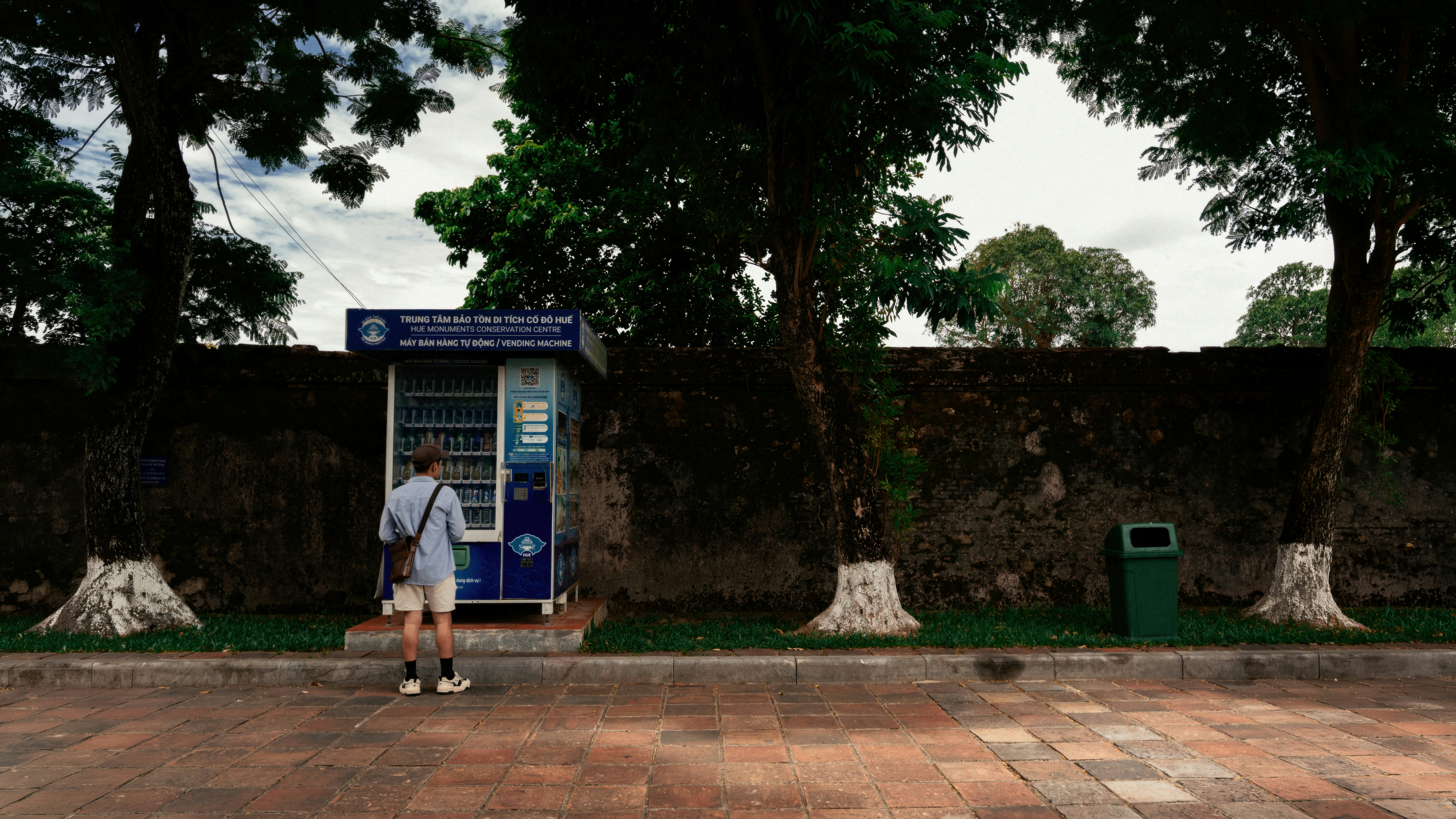 Quiet Street Transit: A solitary visitor at a vending kiosk beside a mossy wall