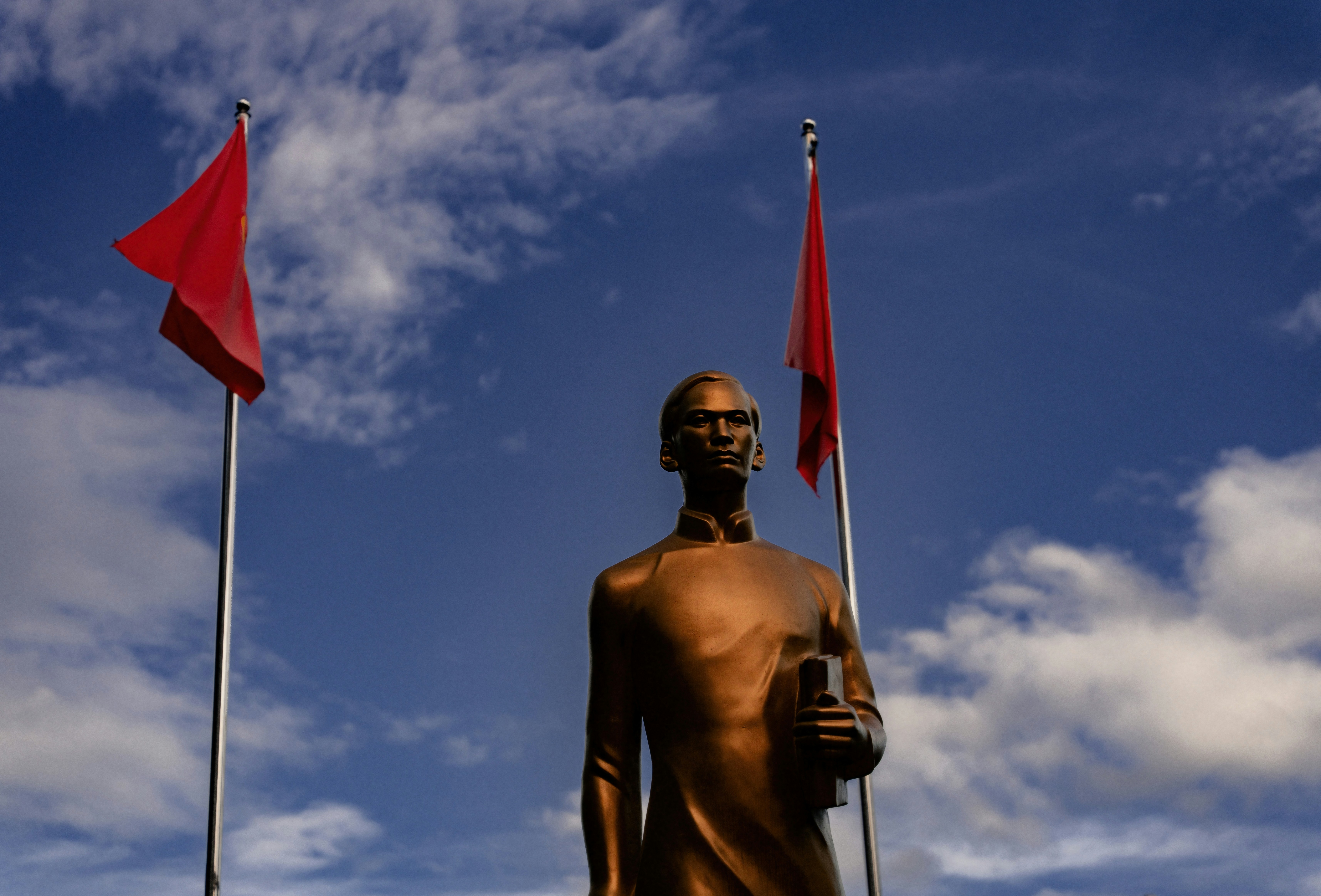 Bronze Sentinel: A Statue Reaching Toward Sky and Flags Under Wide Blue