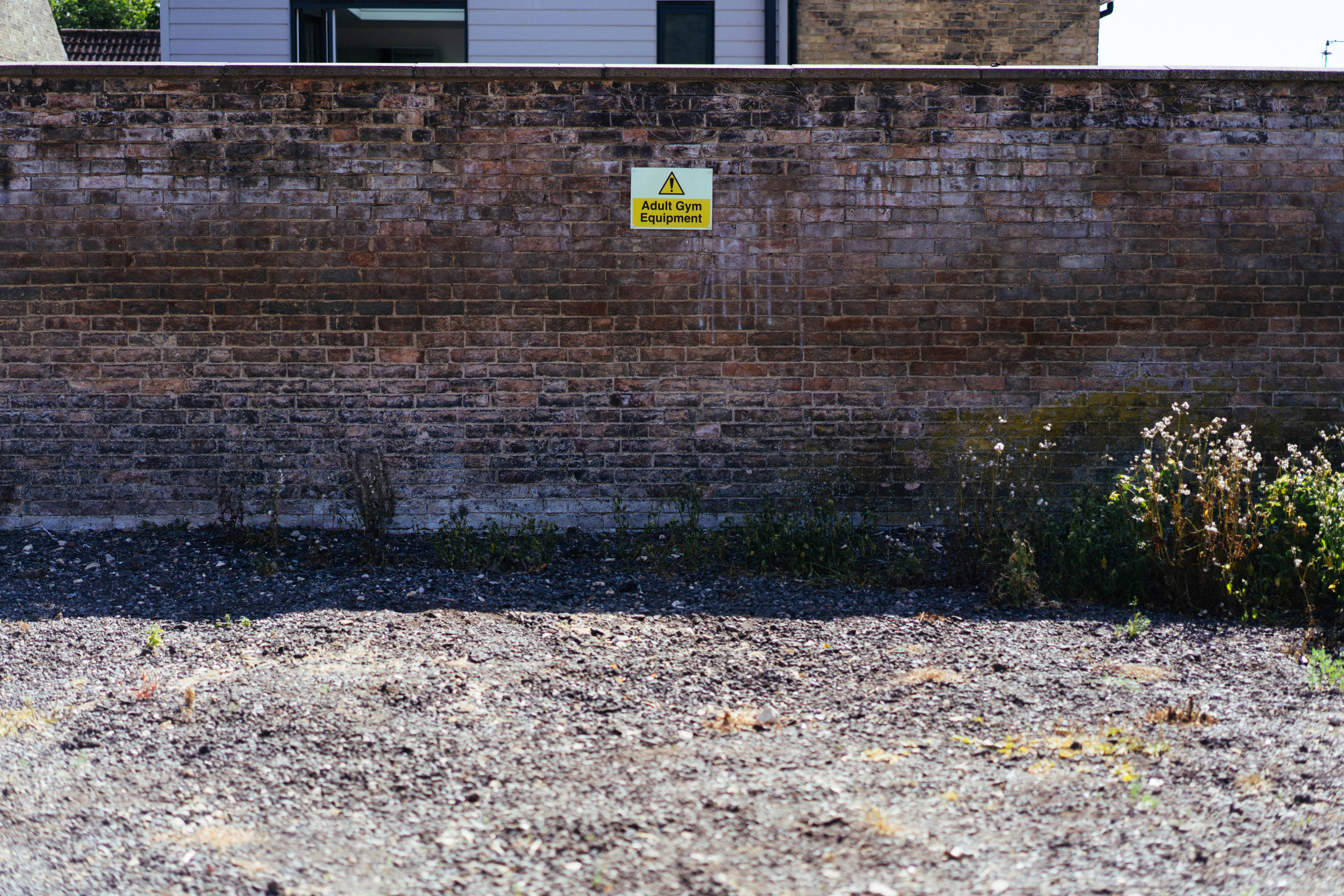 Warning Sign Above Weathered Brick Wall over a Pebble Lot