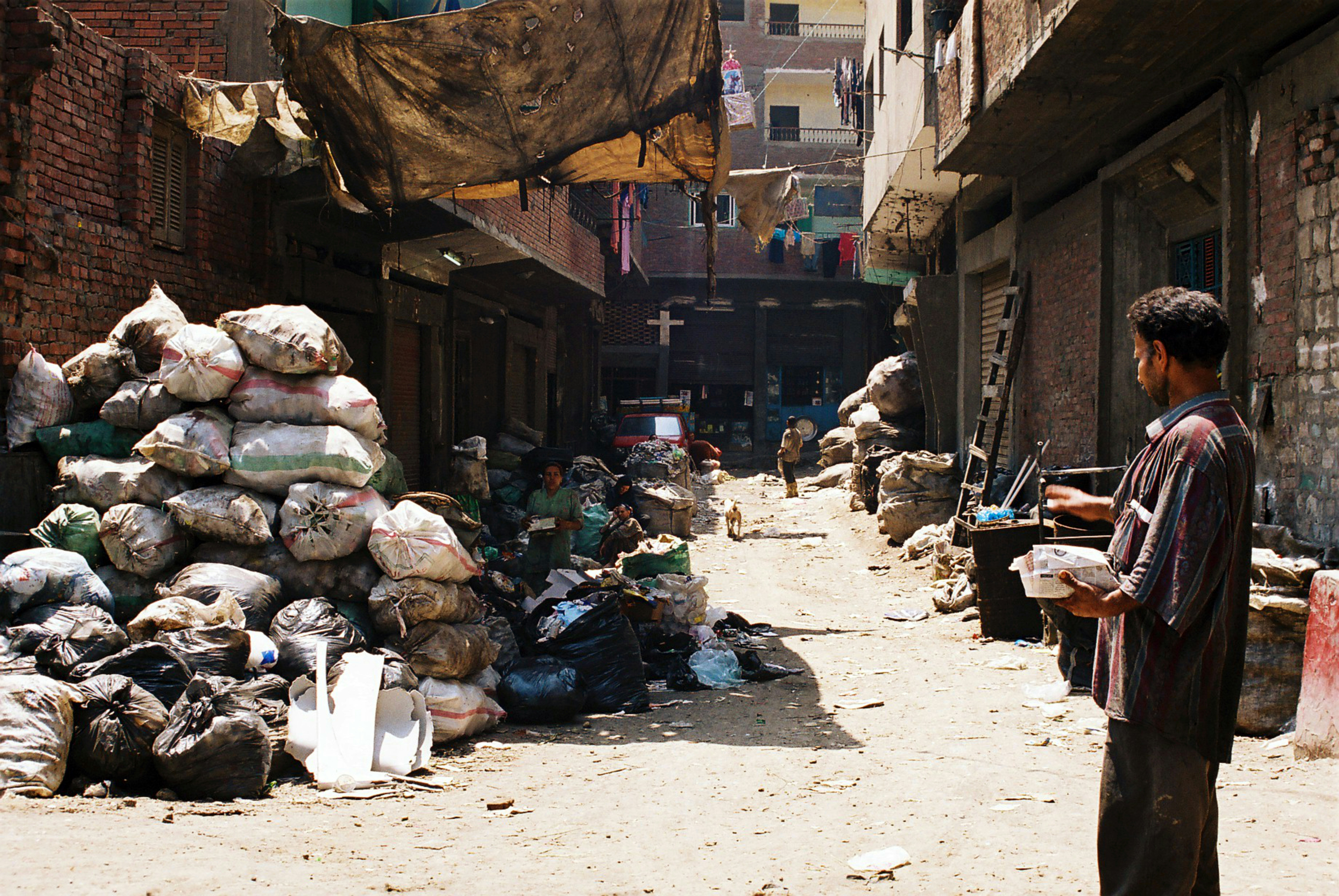 Dusty Alley Portrait: A man with a bowl amid a cluttered waste-strewn street