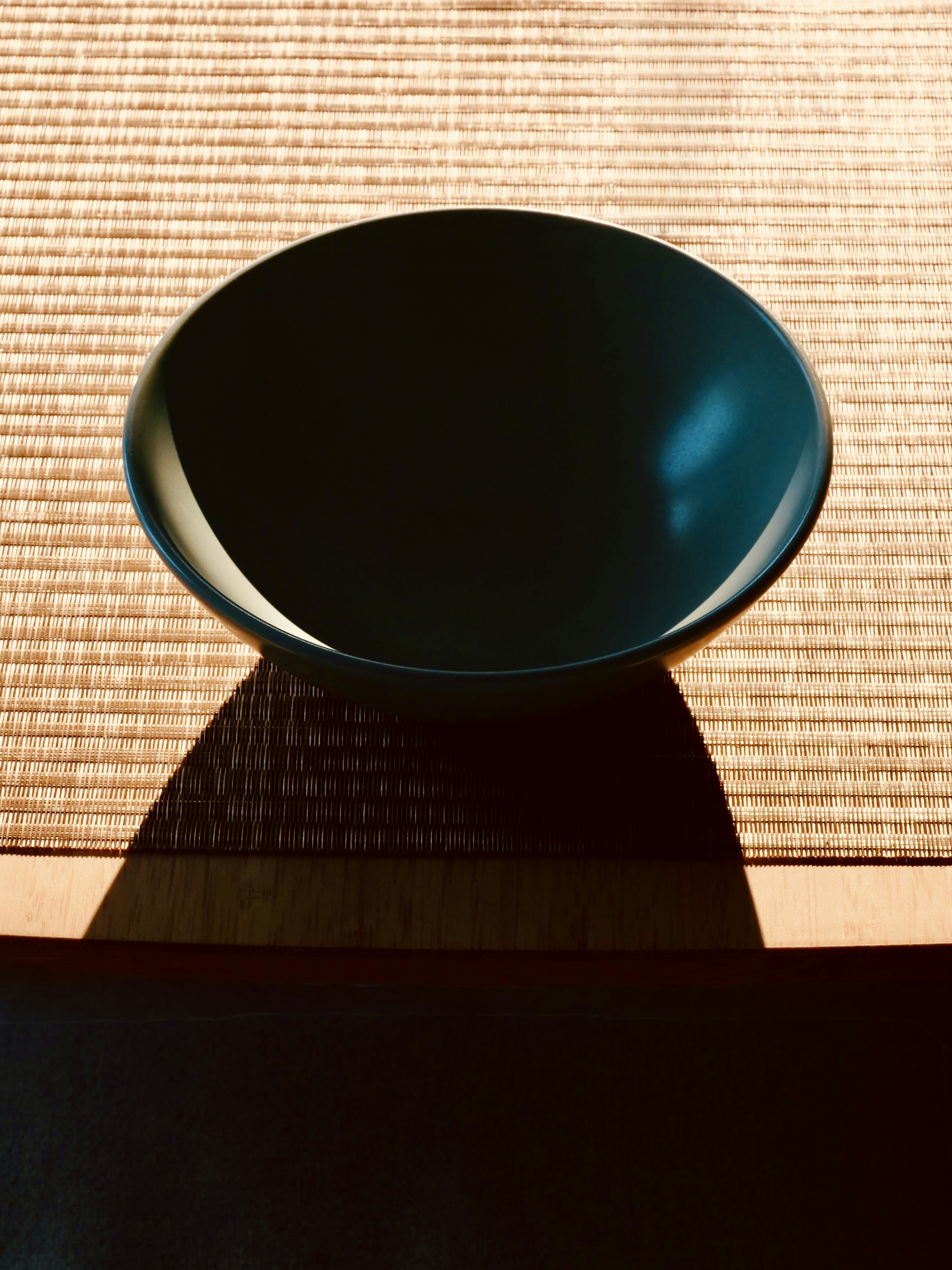 Sunlit Ceramic Bowl Cast in Shadow on a Bamboo Mat