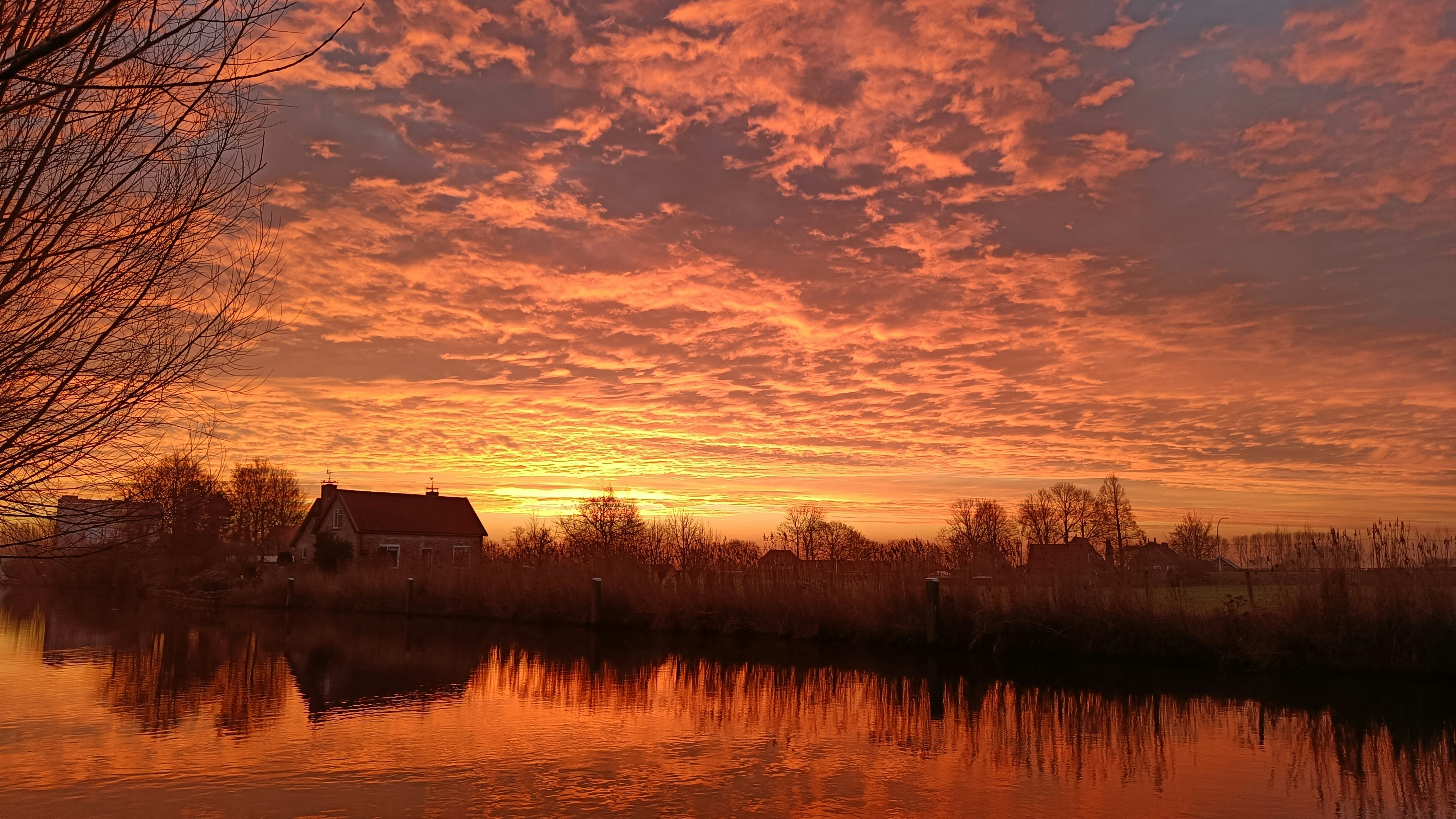Vibrant sunset over a tranquil canal with silhouetted houses.