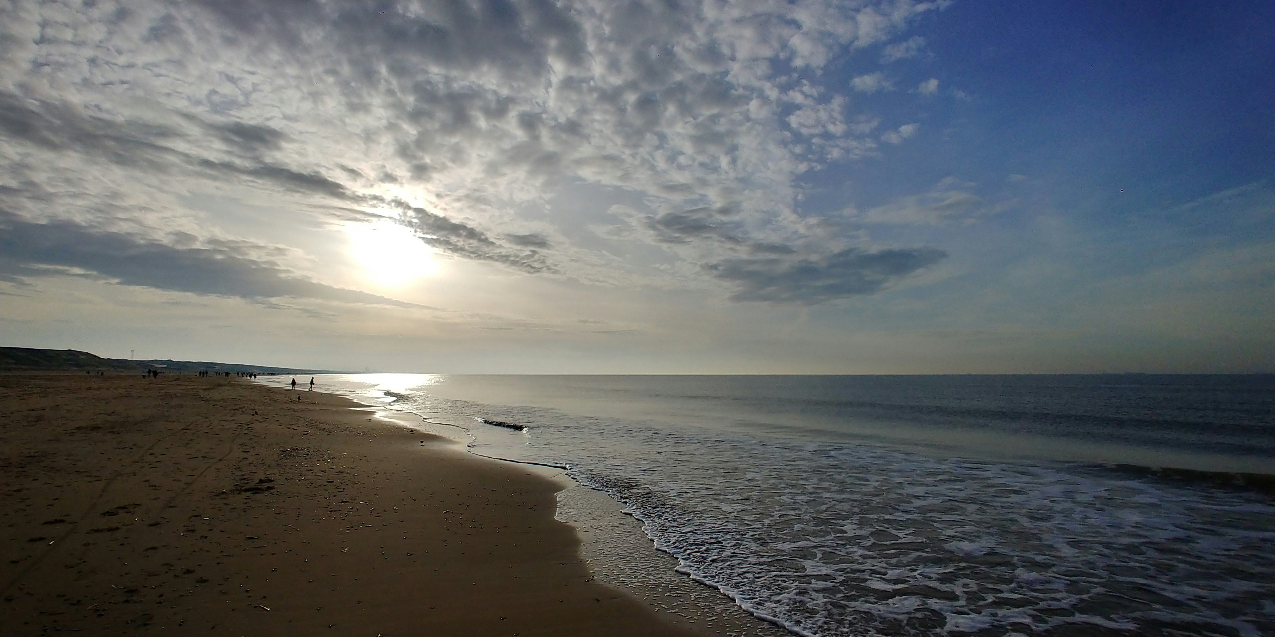 Sunlit shoreline with gentle waves and a distant figure near the water's edge, emphasizing quiet coastal mood. This is a photographic capture of a beach scene.