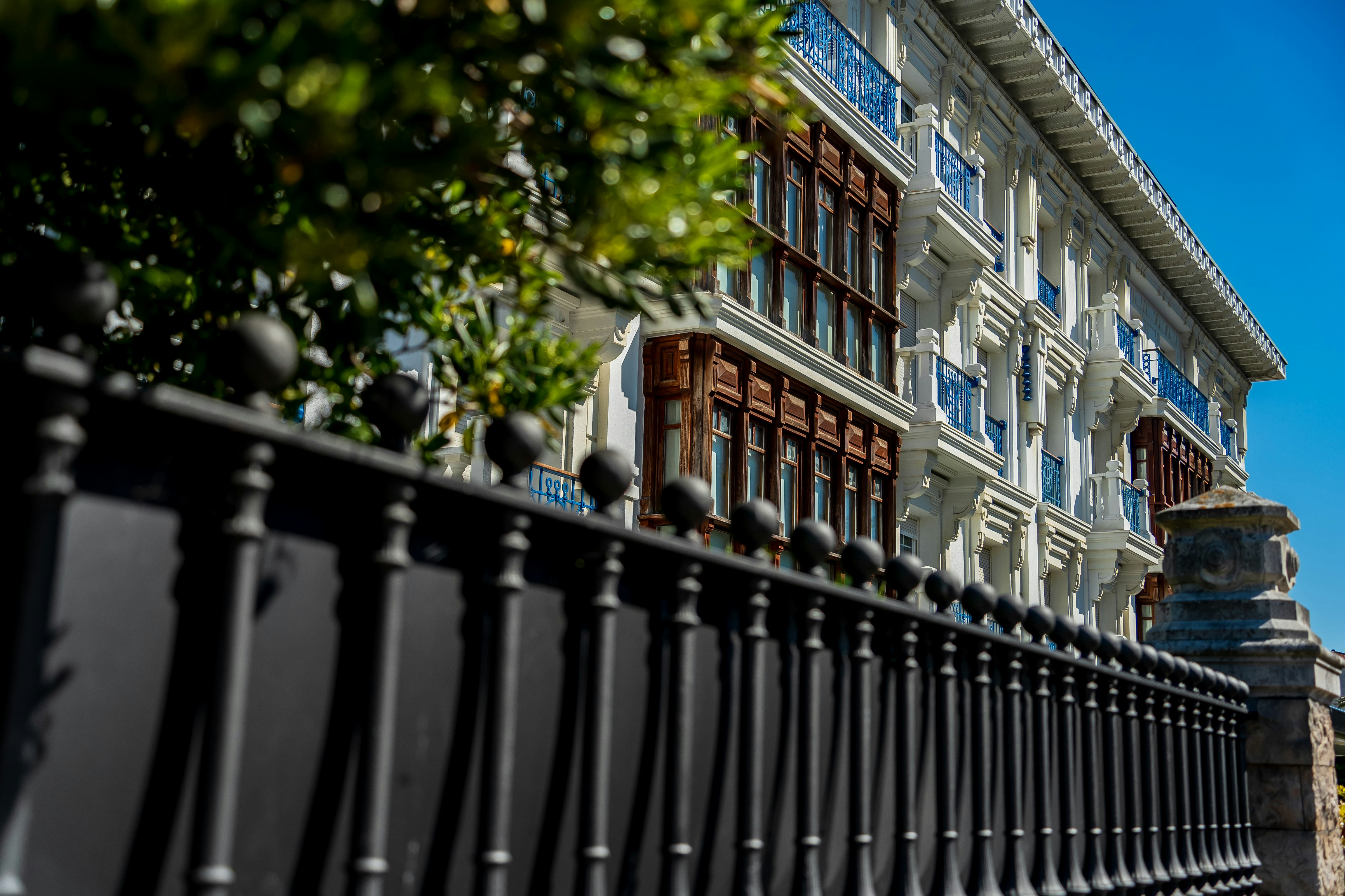 Iron-rimmed railing leads the eye toward a sunlit terrace of classic townhouses