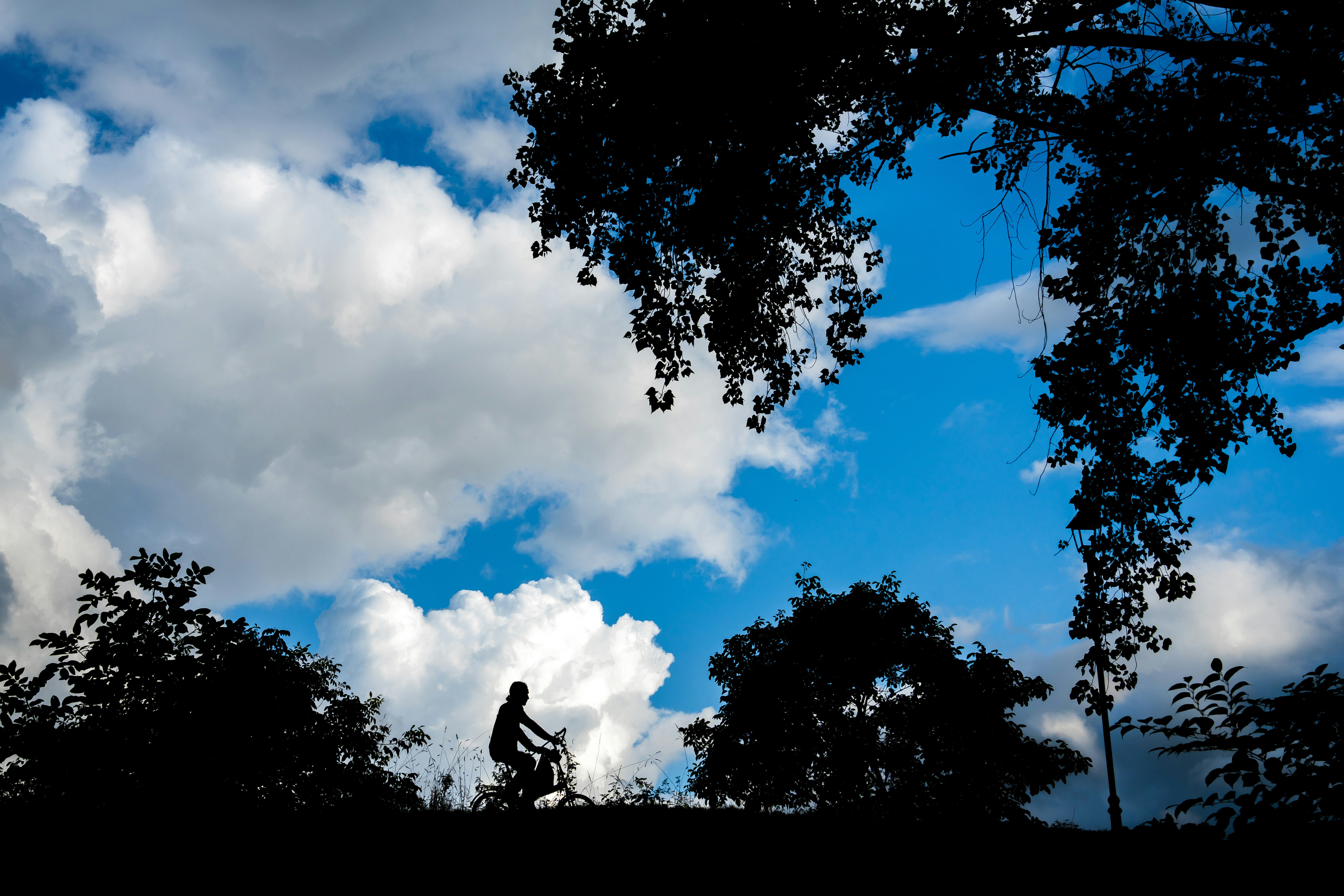 Silhouette Ride: A Cyclist Traverses the Hill Against a Sky of Clouds