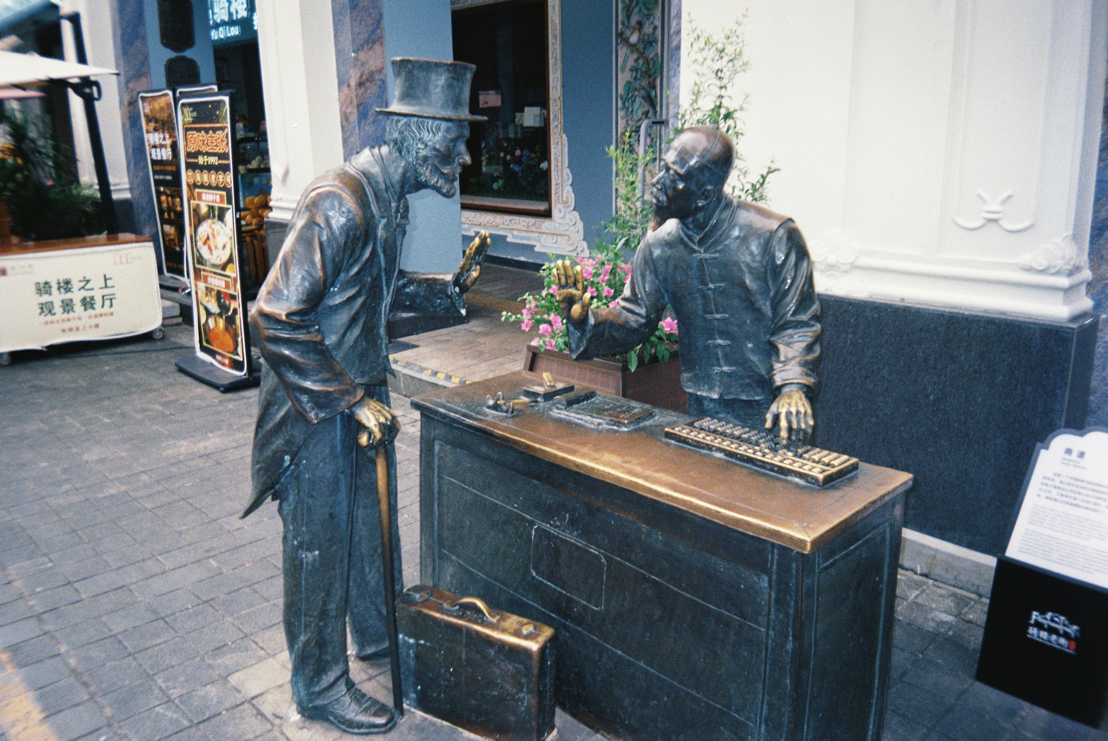 Street statues of men in top hat and behind counter.