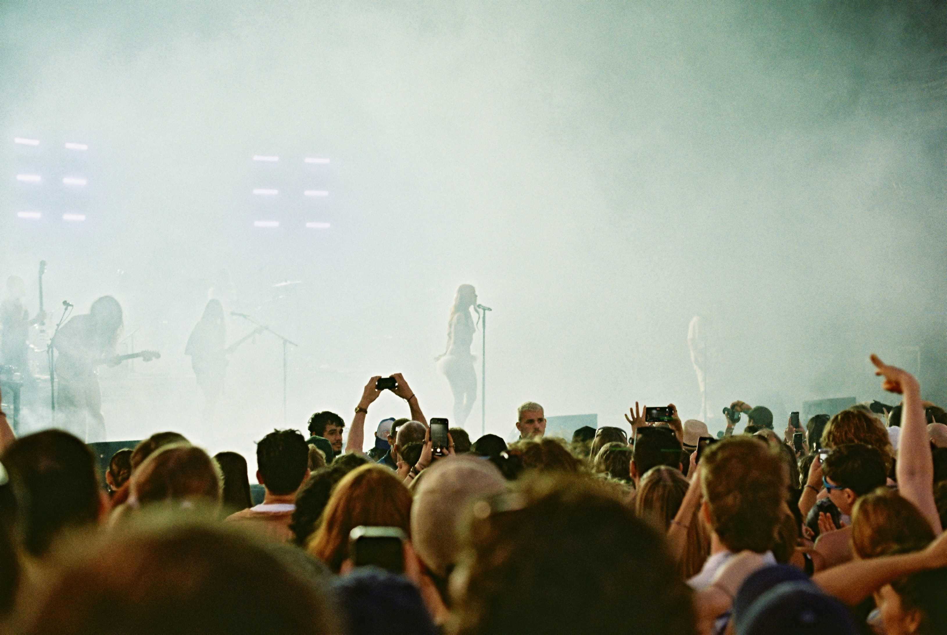 Band silhouettes and a singer at the mic dissolve into a wall of pale festival smoke.