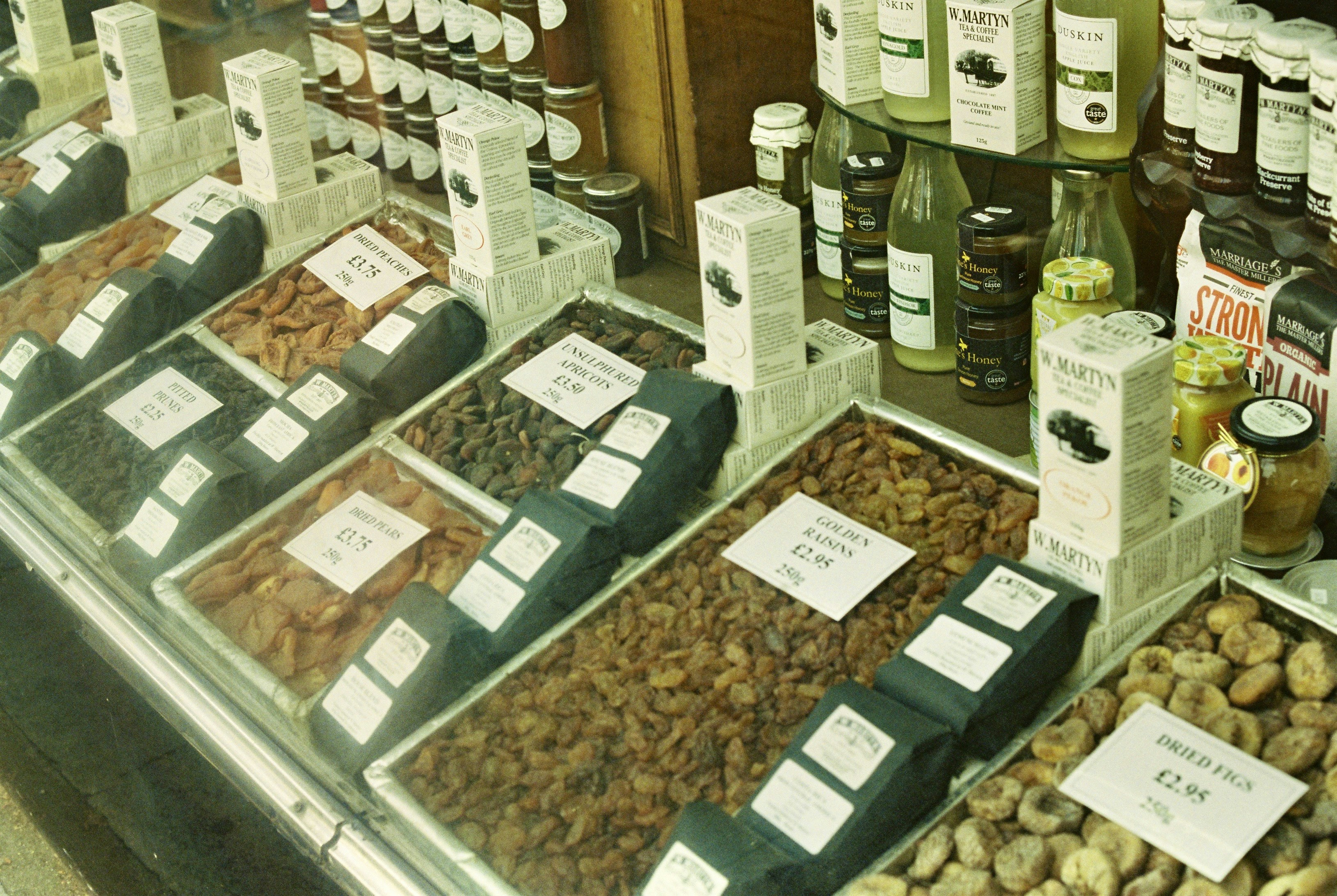 Assorted nuts and bottled goods arranged in a shop display, with clear plastic bins and labeled packaging.