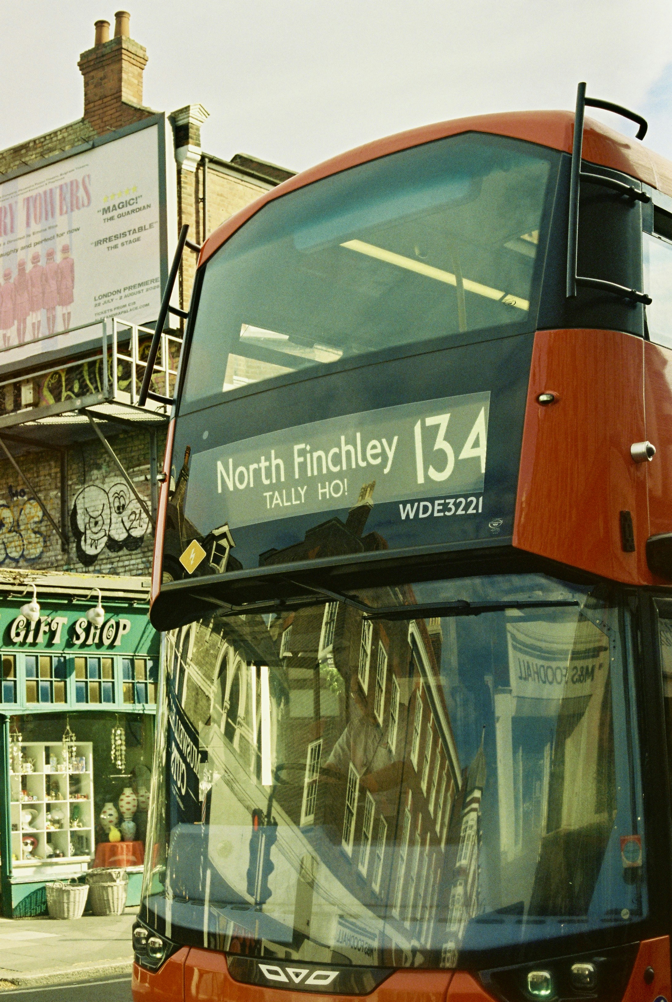 The front of a red London double-decker bus fills the frame, its destination sign glowing above a vintage gift shop.