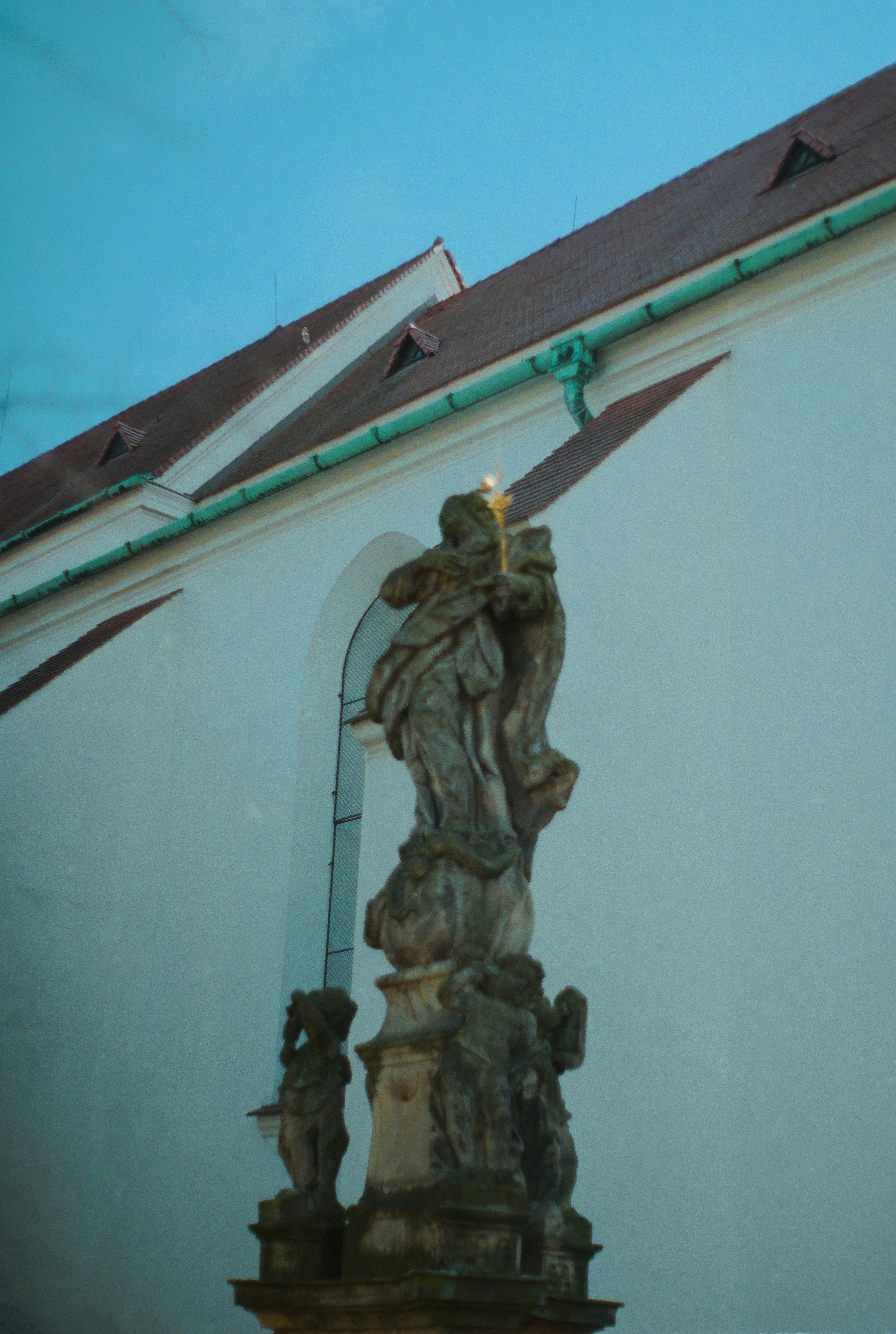 Weathered statue in front of a pale church under a bright blue sky