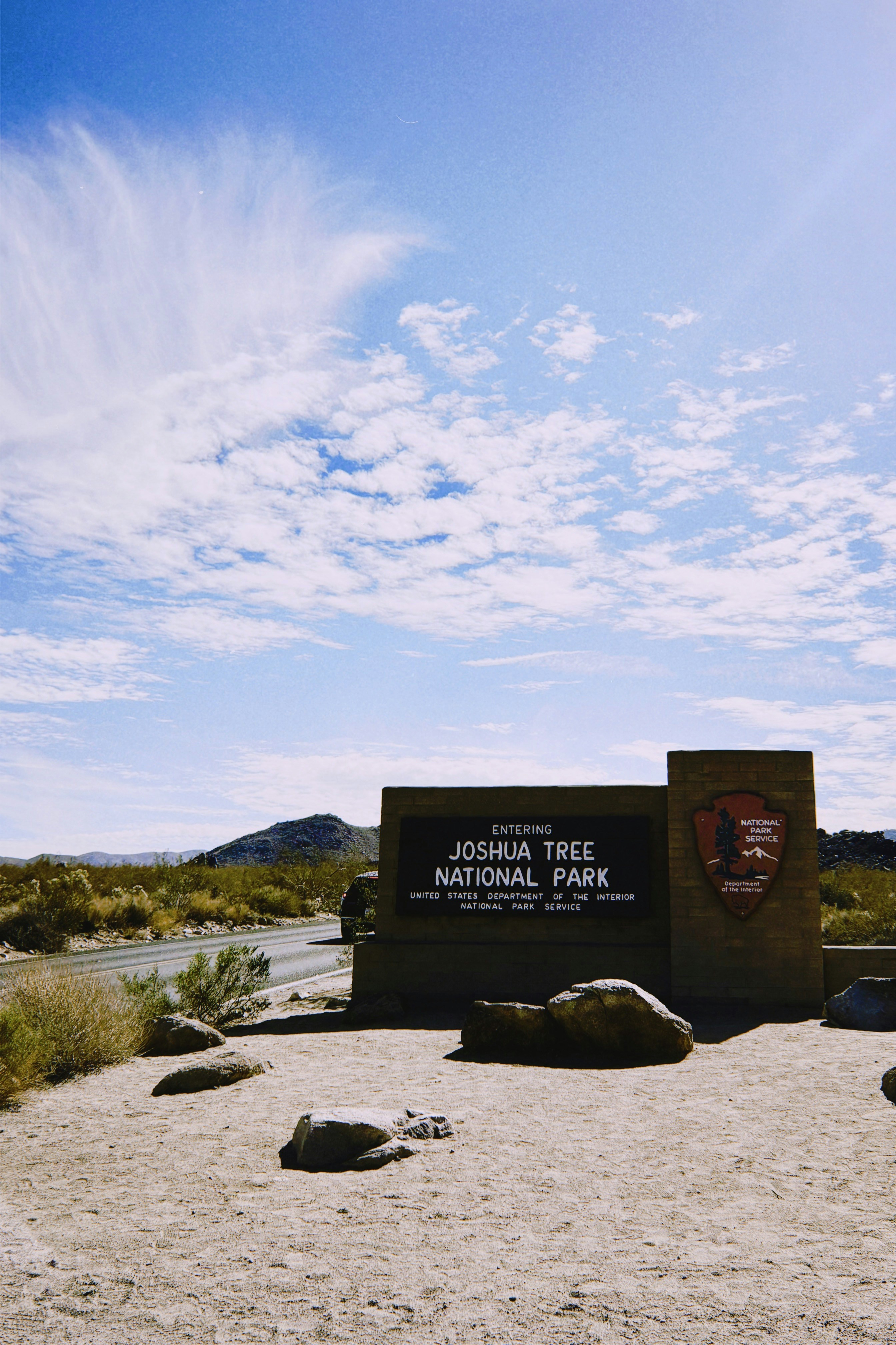Welcome sign at Joshua Tree National Park with desert foreground and blue sky; a landscape shot featuring the entrance monument and surrounding terrain.