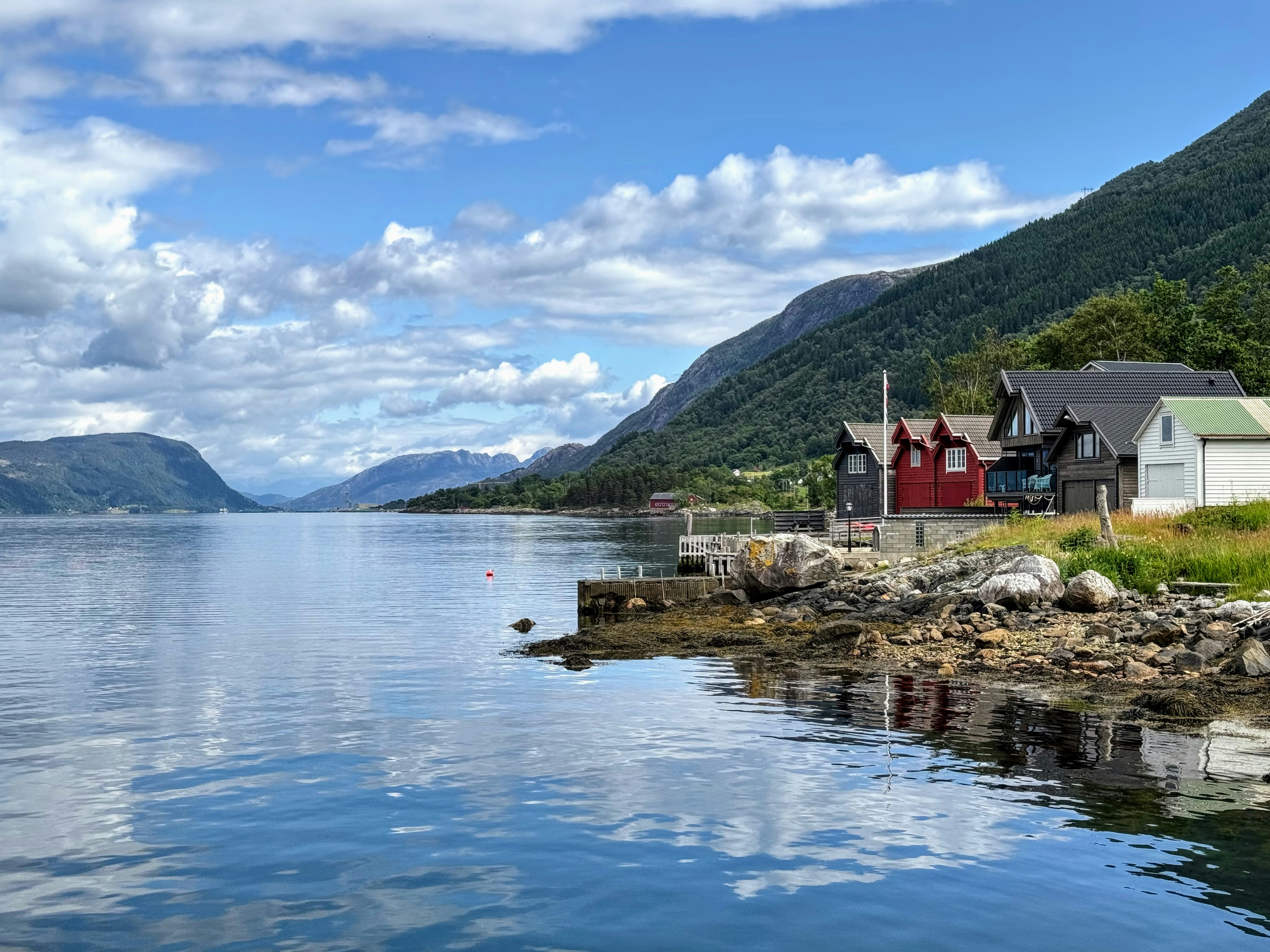 Colorful lakeside cottages cling to rocky shore under a sky of scattered clouds