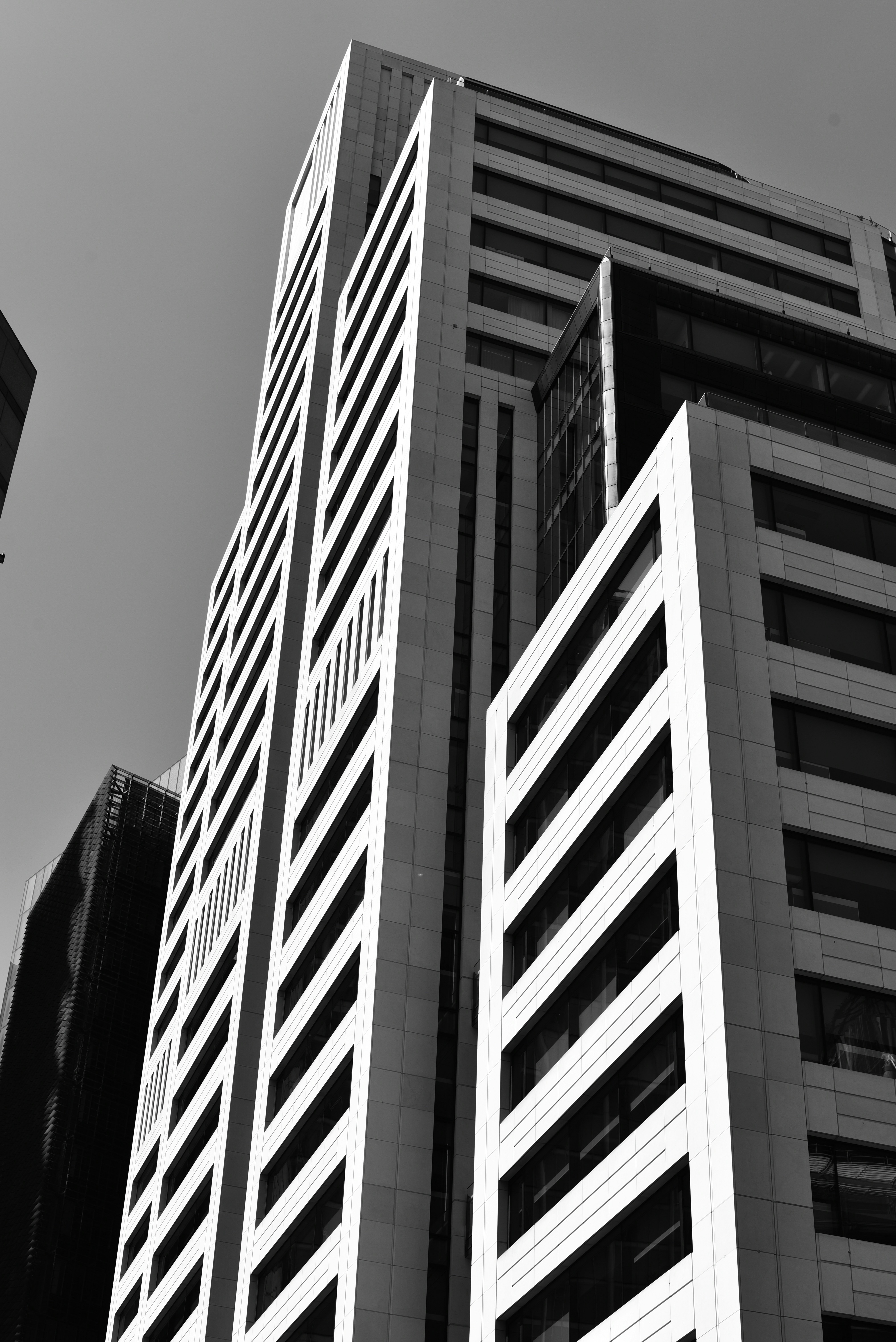 A grayscale cityscape shows towering modern buildings with bold geometric lines and deep shadows.