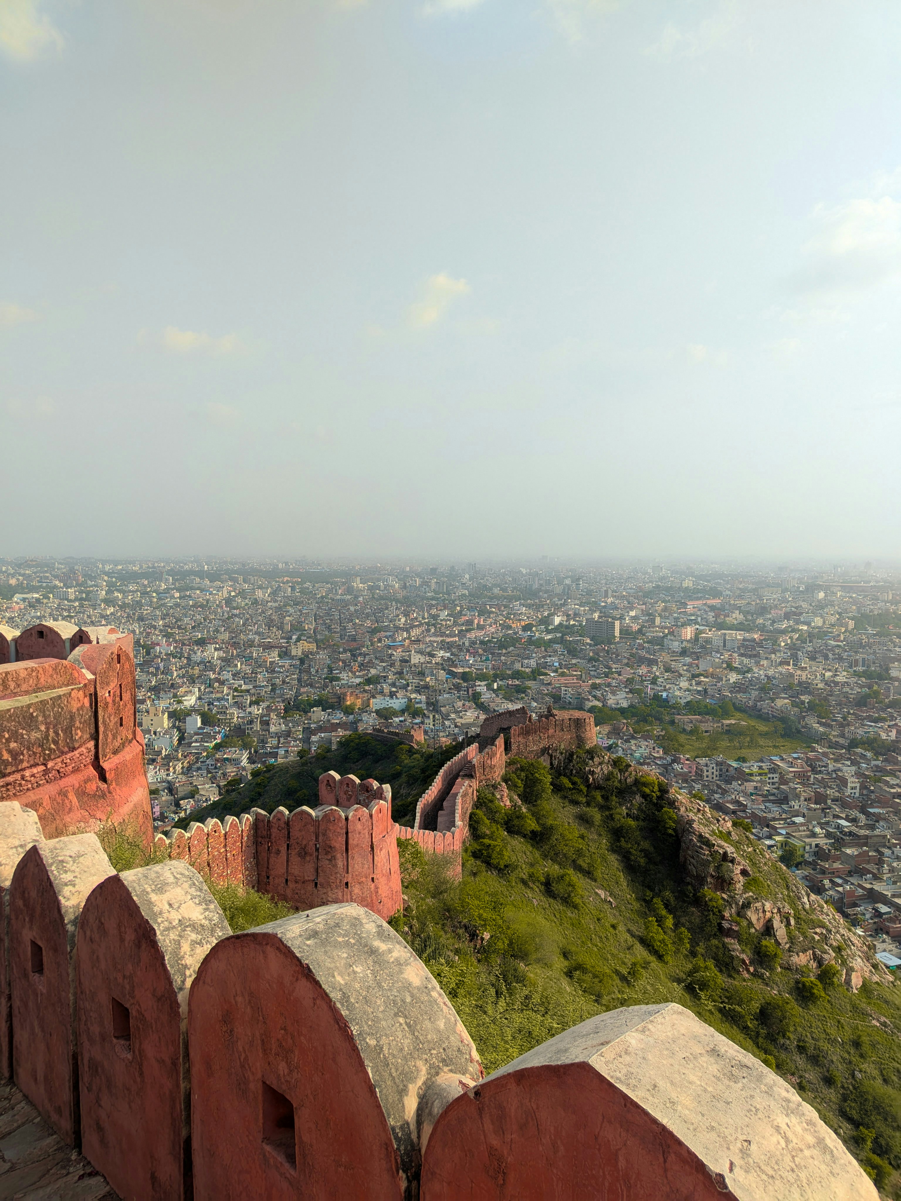 Ancient red fort wall overlooking a sprawling hazy city.