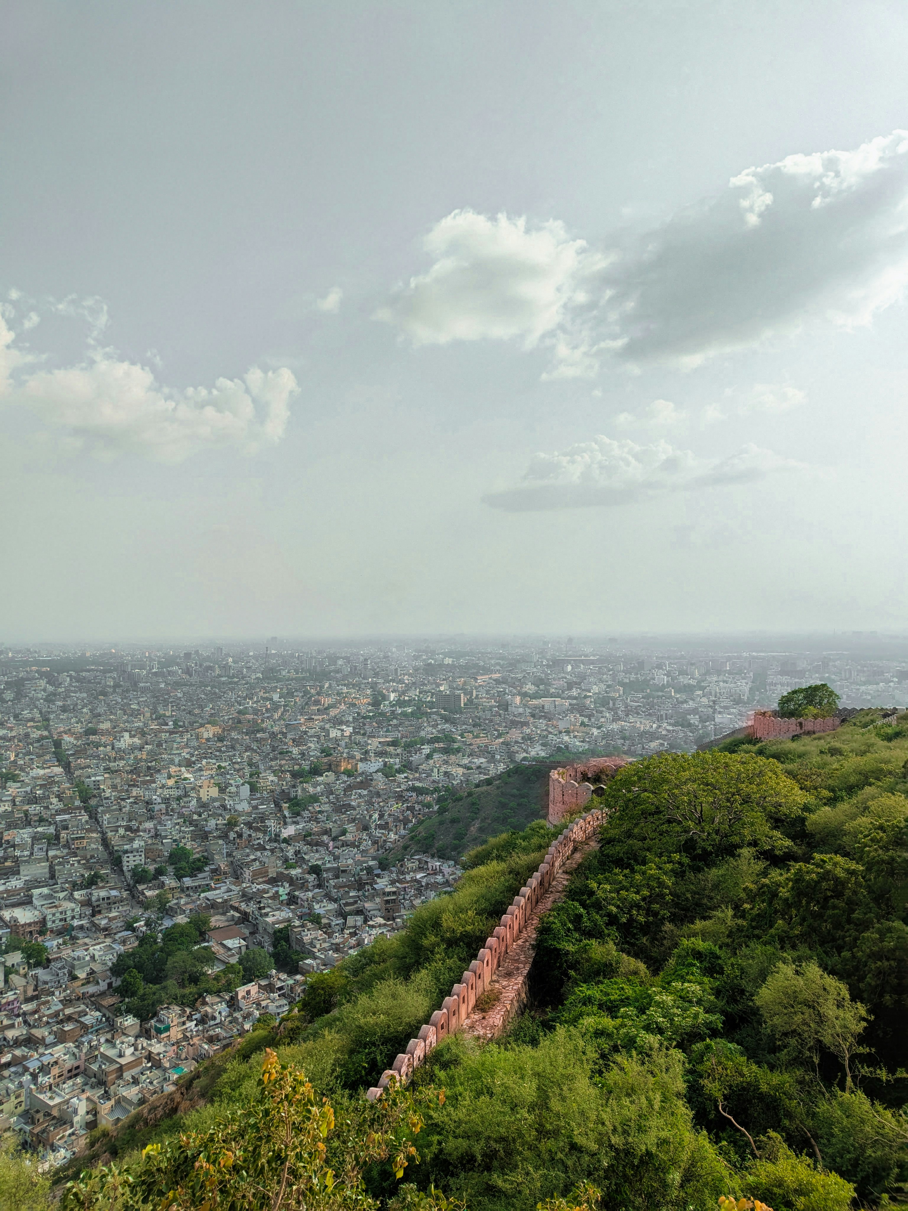 Ancient wall on a green hill overlooking a vast city.