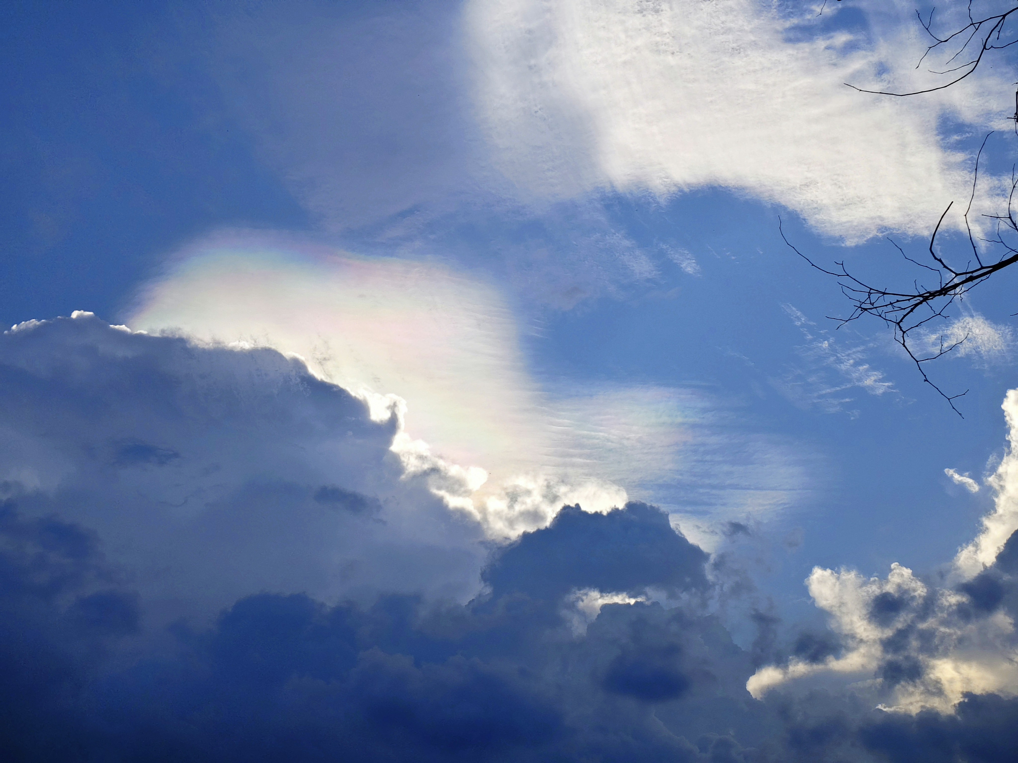 Rainbow-diffused sunlit cloud over a moody blue sky