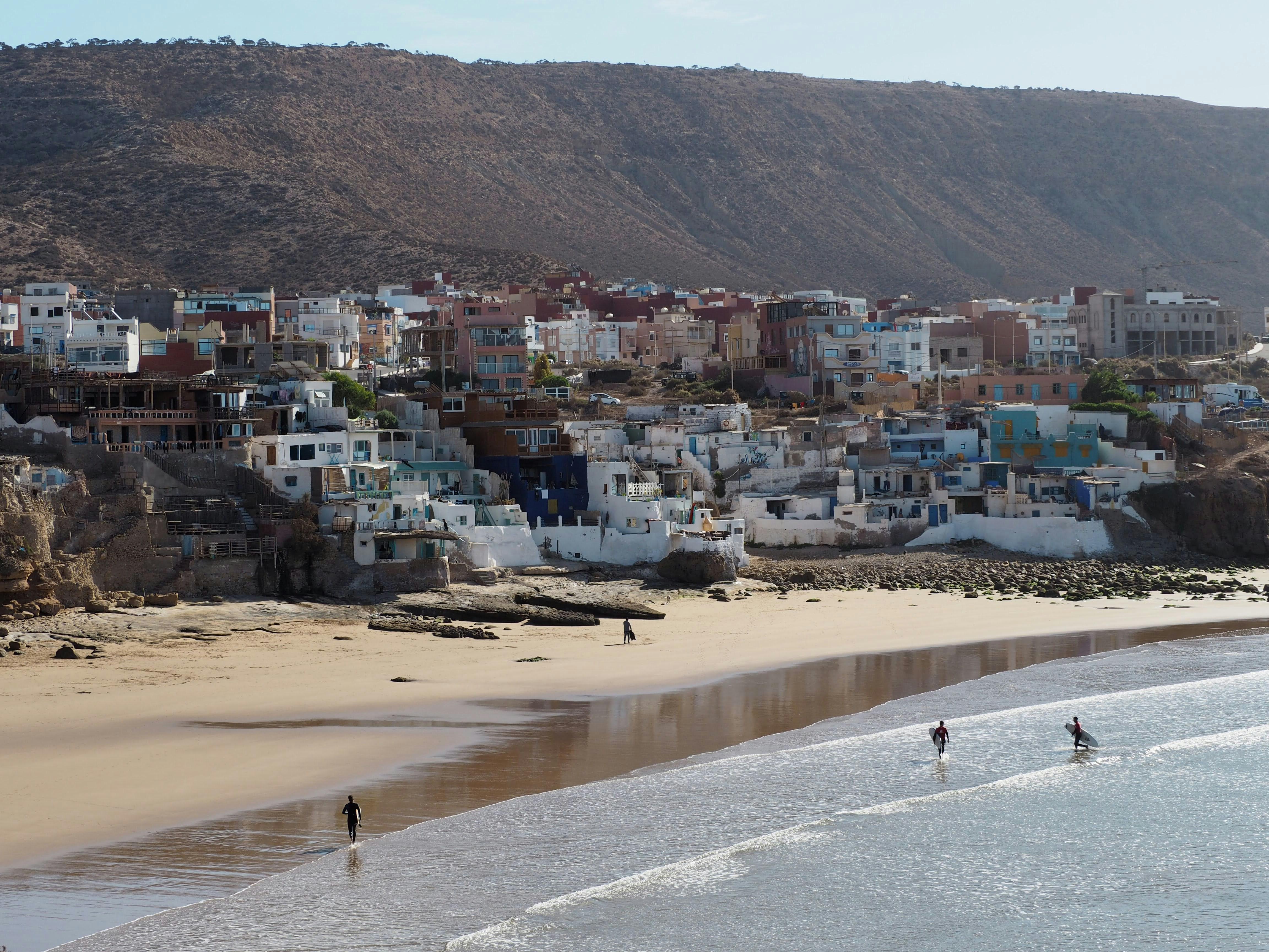 Colorful hillside buildings line the coastline with a sandy beach and gentle surf in the foreground.