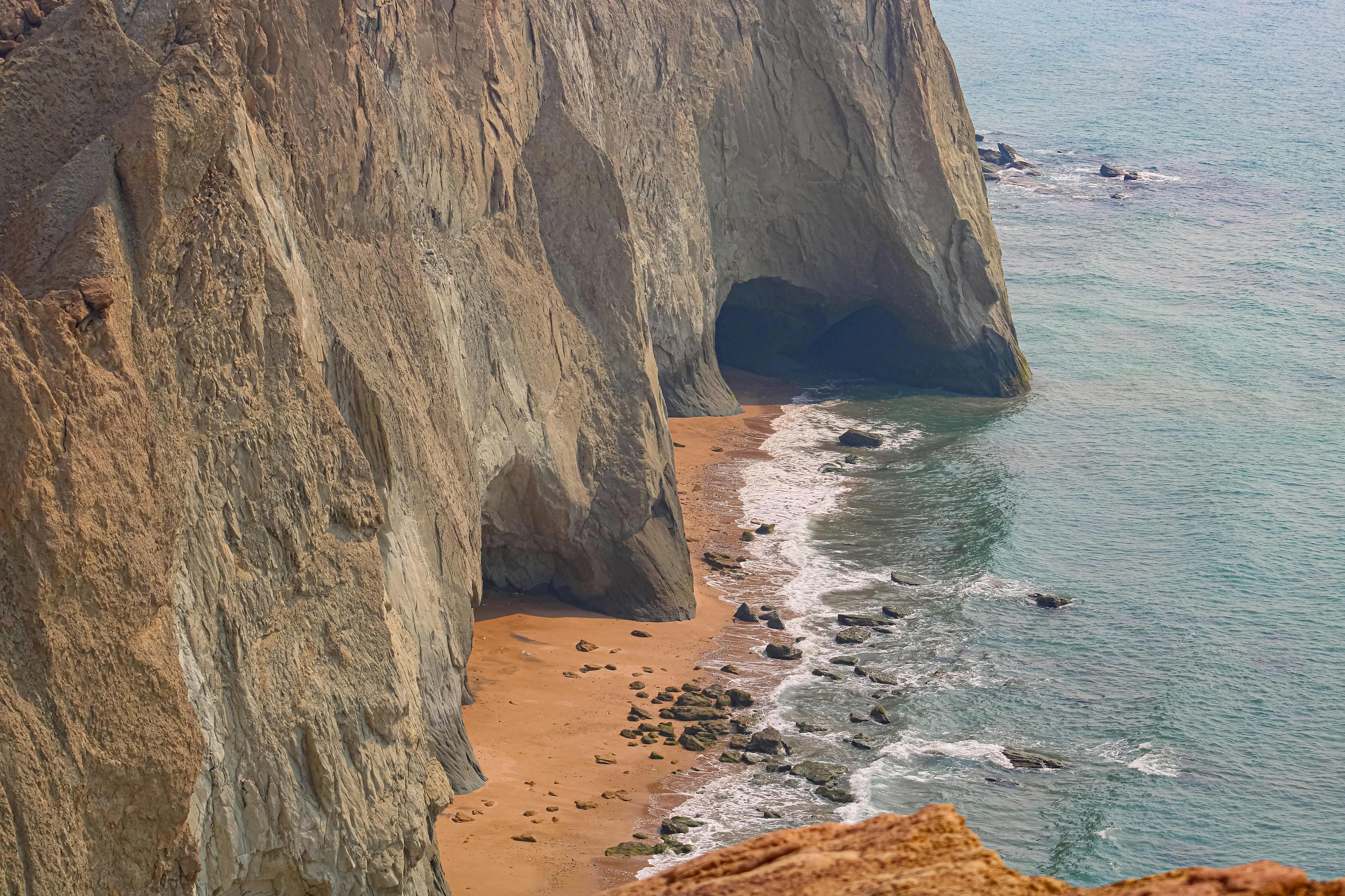 Coastal Cliffs Carved by Tide: A Secluded Cave and Sandy Verge