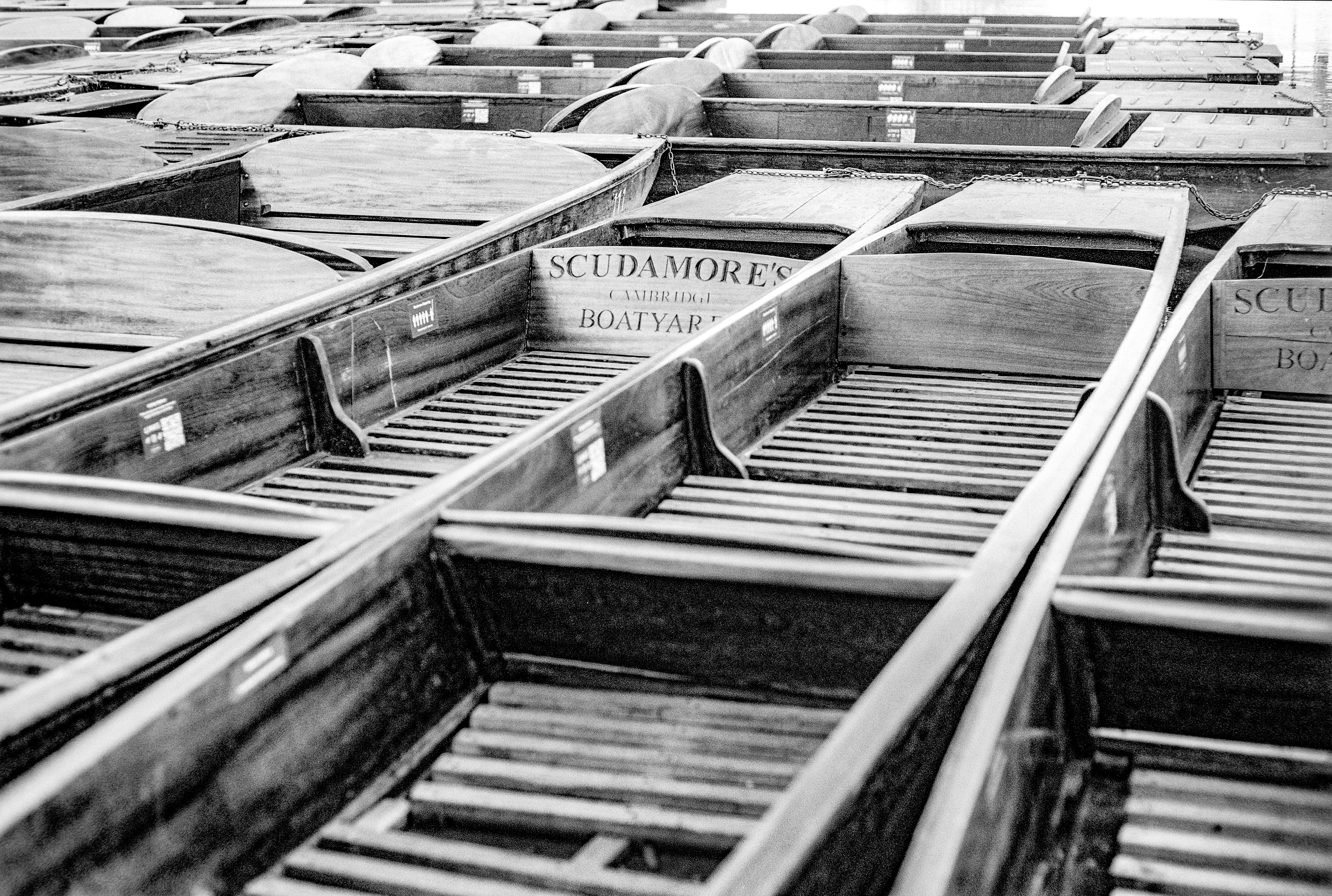 Row of wooden boats packed tightly together, captured in grayscale to emphasize texture and pattern; a minimal, cropped view highlighting the hulls and planks.
