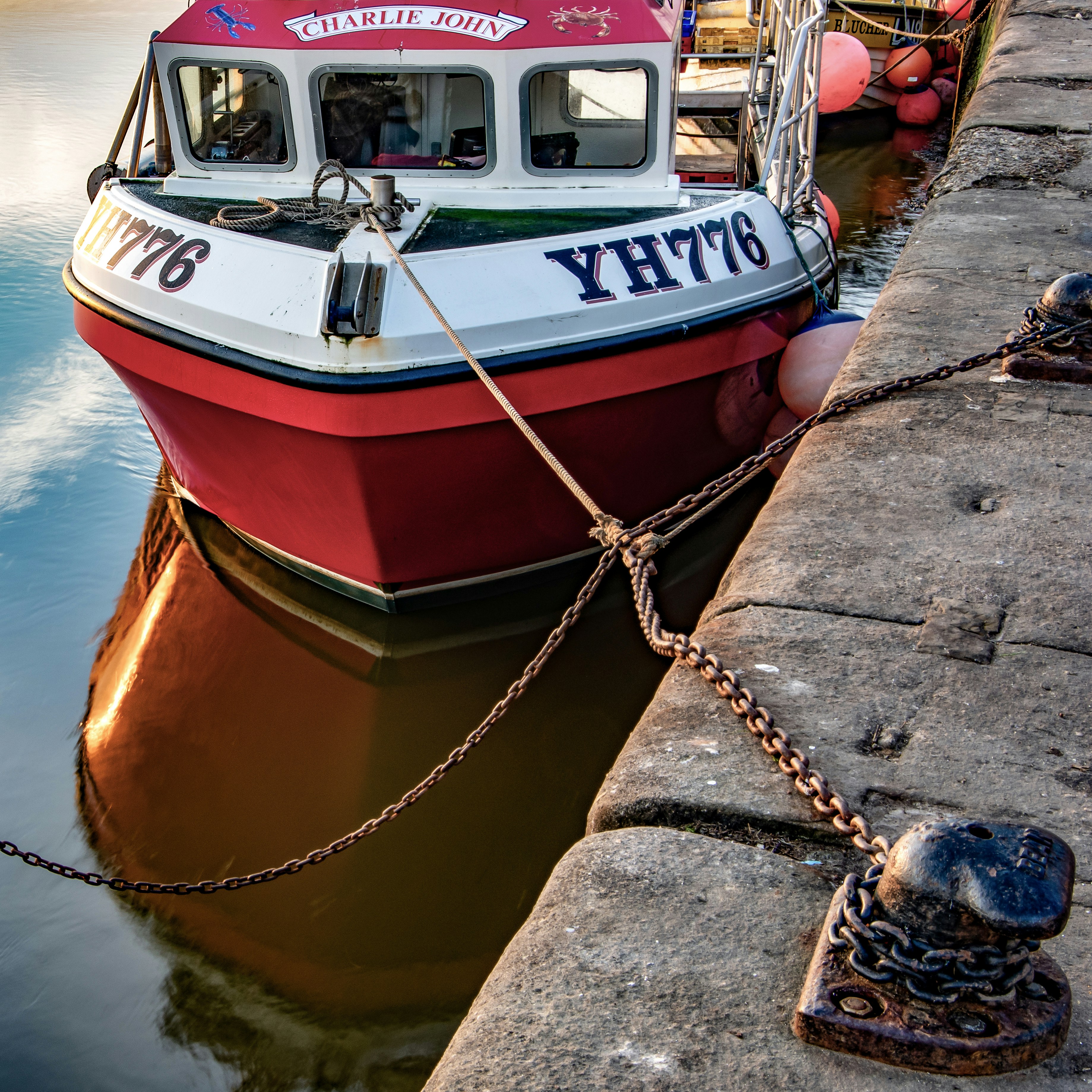 Red-and-white boat tied to a stone dock with weathered chains and calm water reflecting the hull.