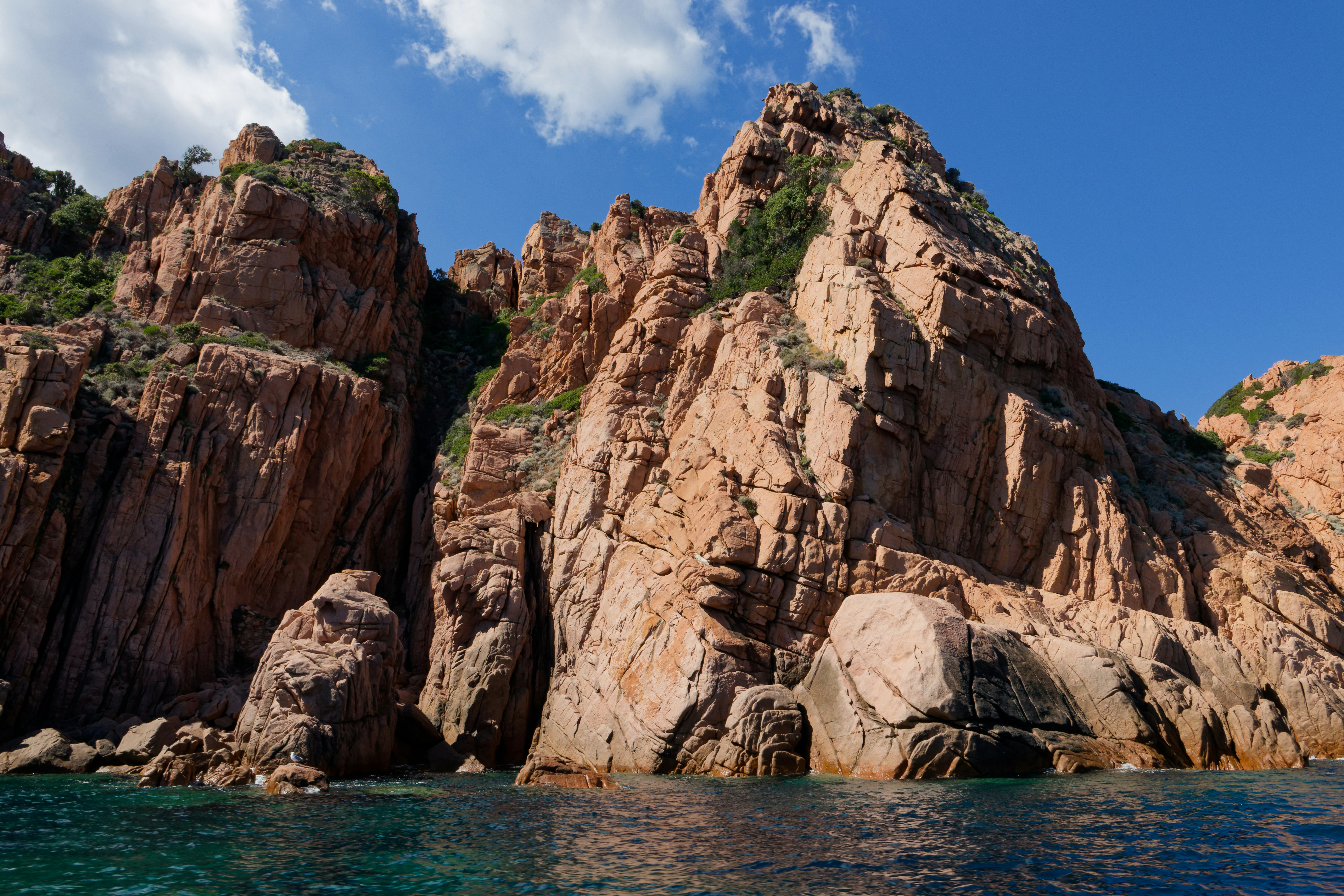 Towering red rock cliffs rise from the calm blue sea.