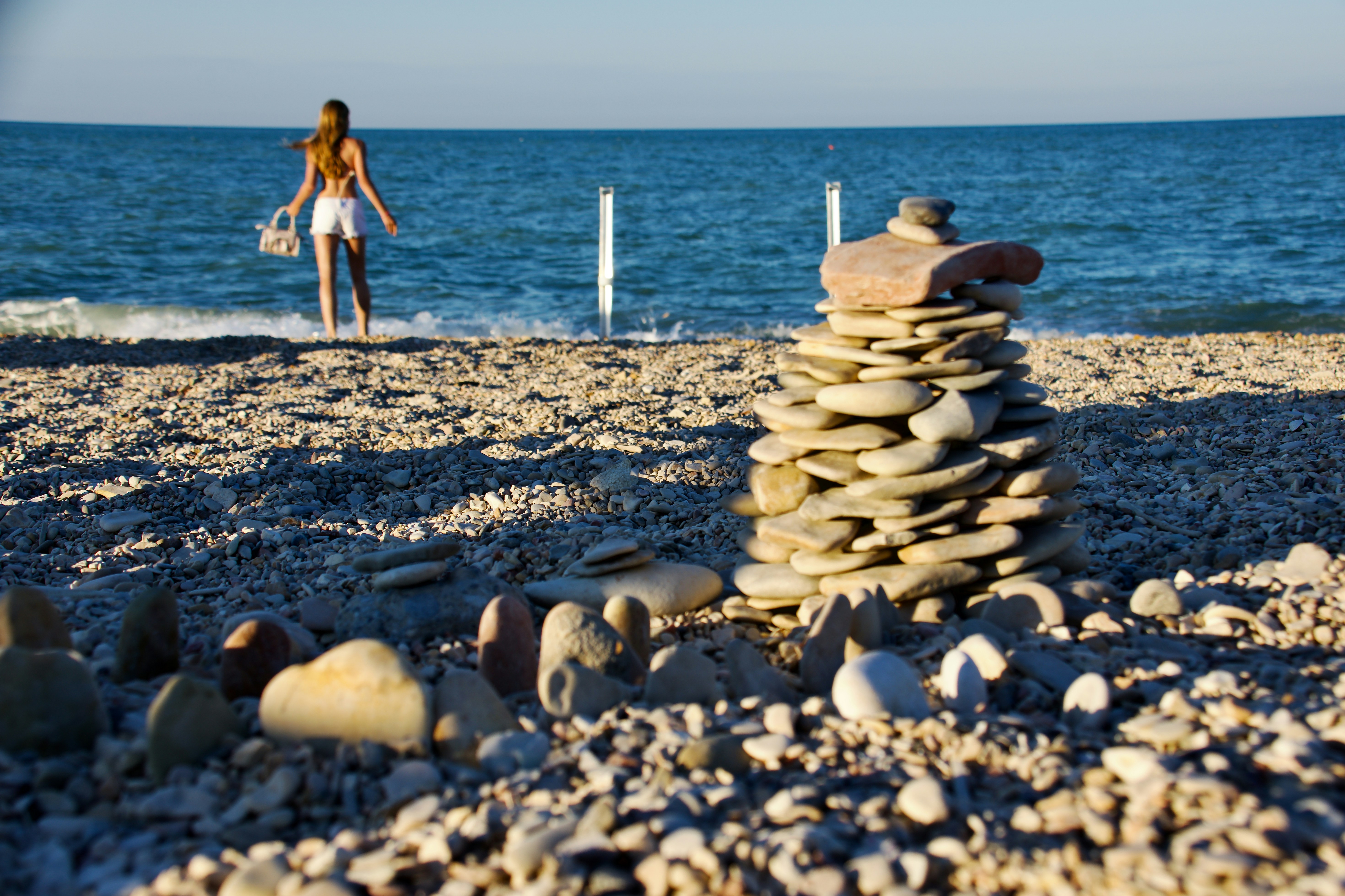 Stacked stones on a rocky beach, person walking towards ocean.