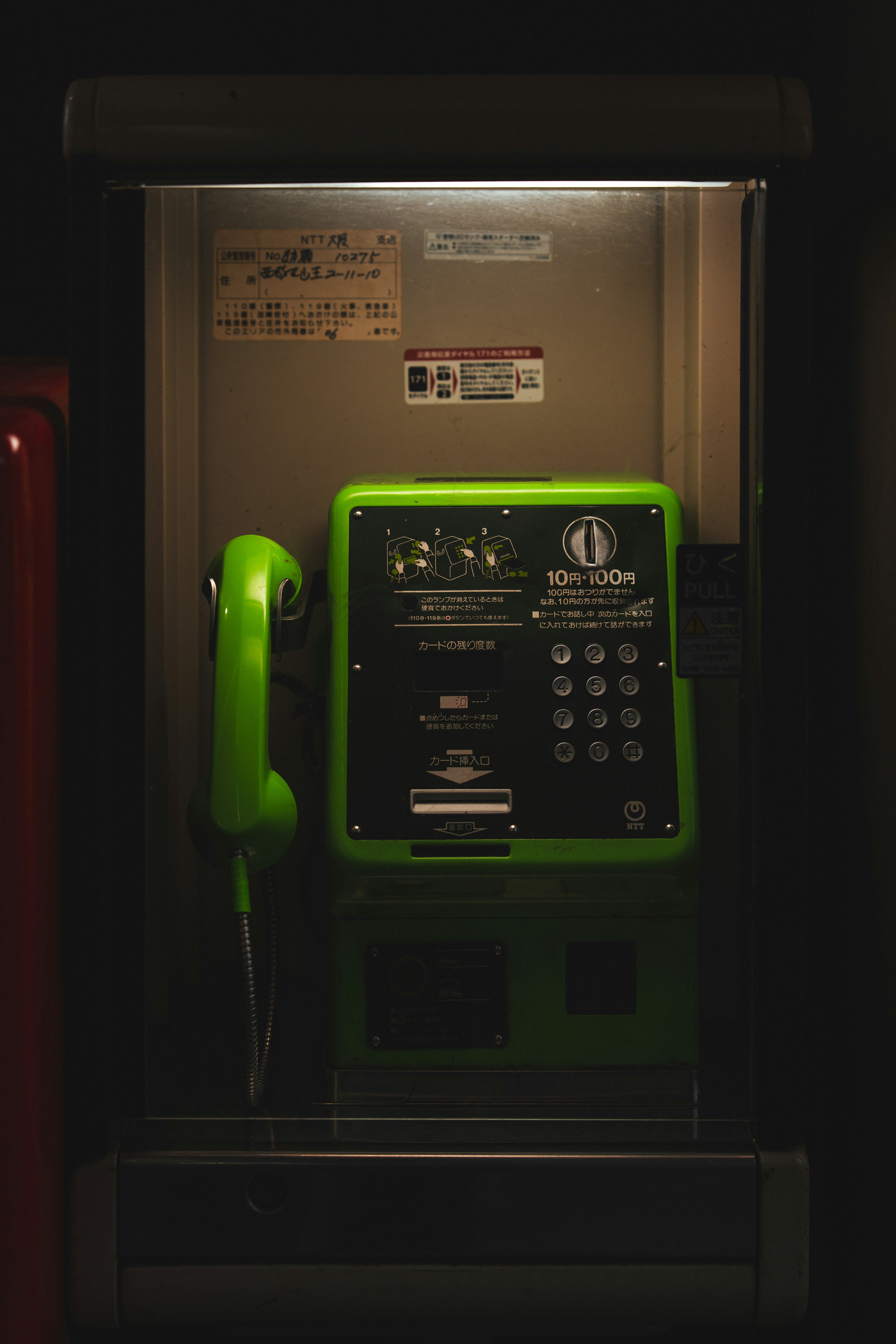 A green public payphone inside a dimly lit booth.