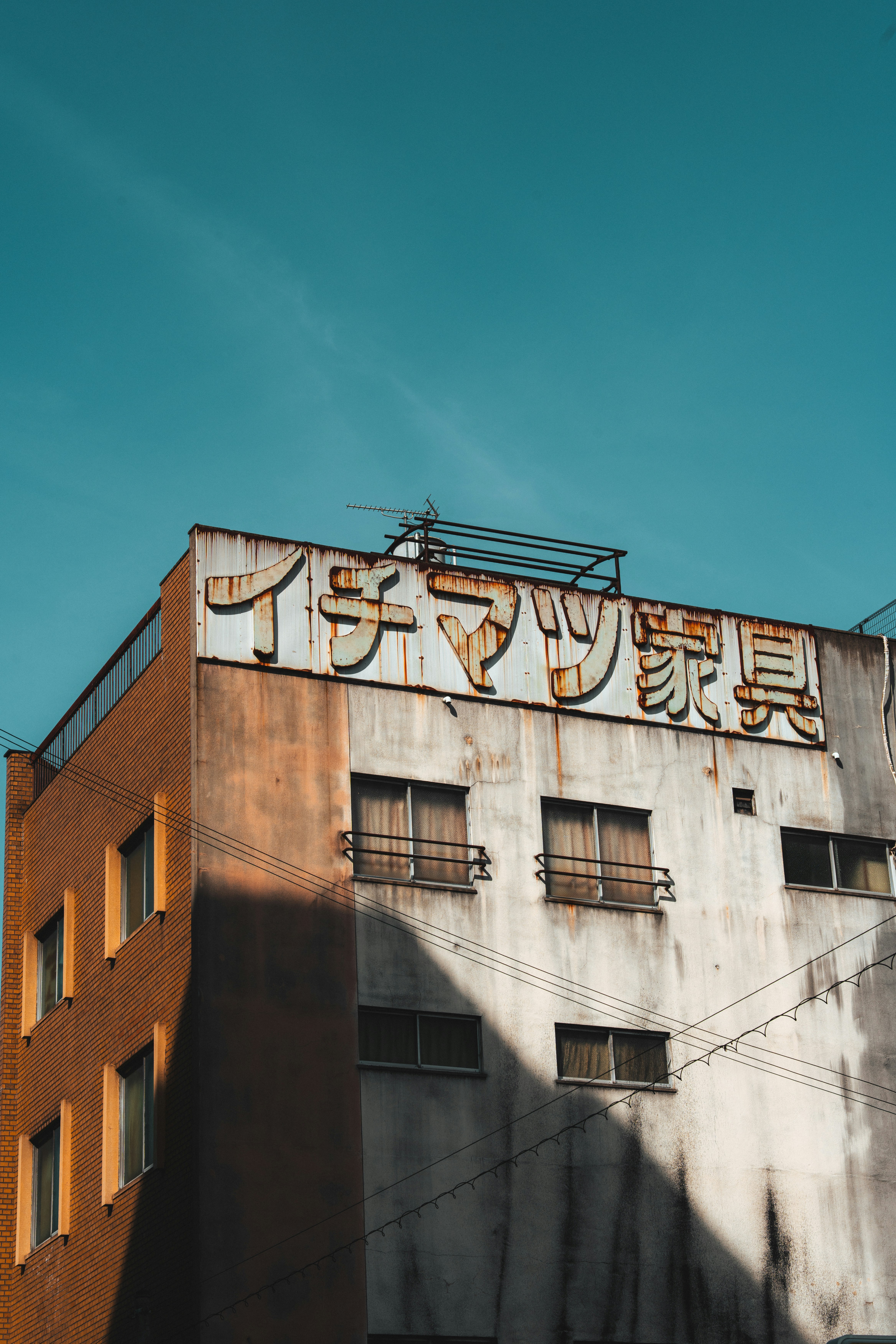 Aged façade under a clear blue sky: Japanese signage atop a sunlit building